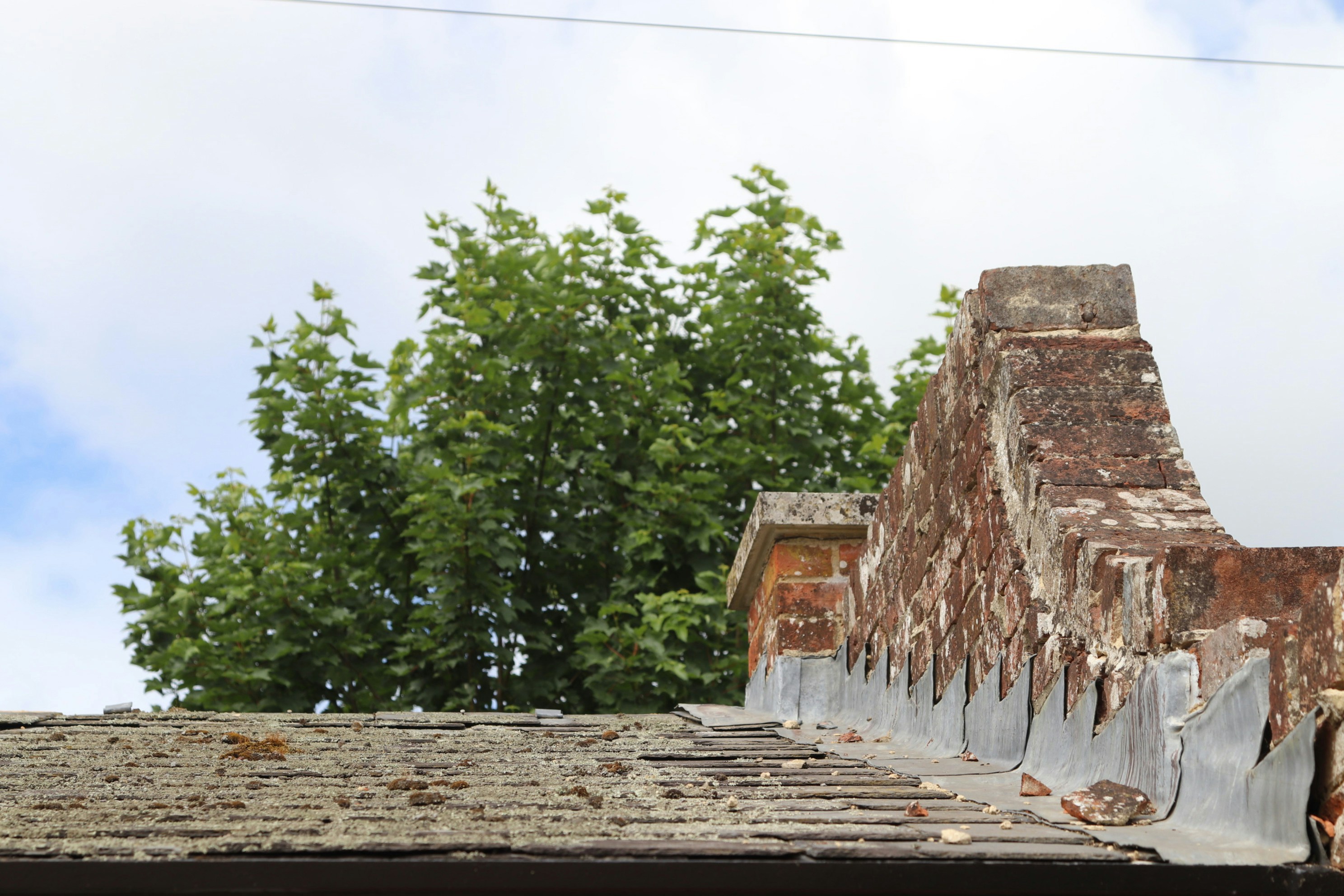 Brick Chimney Rising Above Weathered Roof Tiles at Dappled Sky
