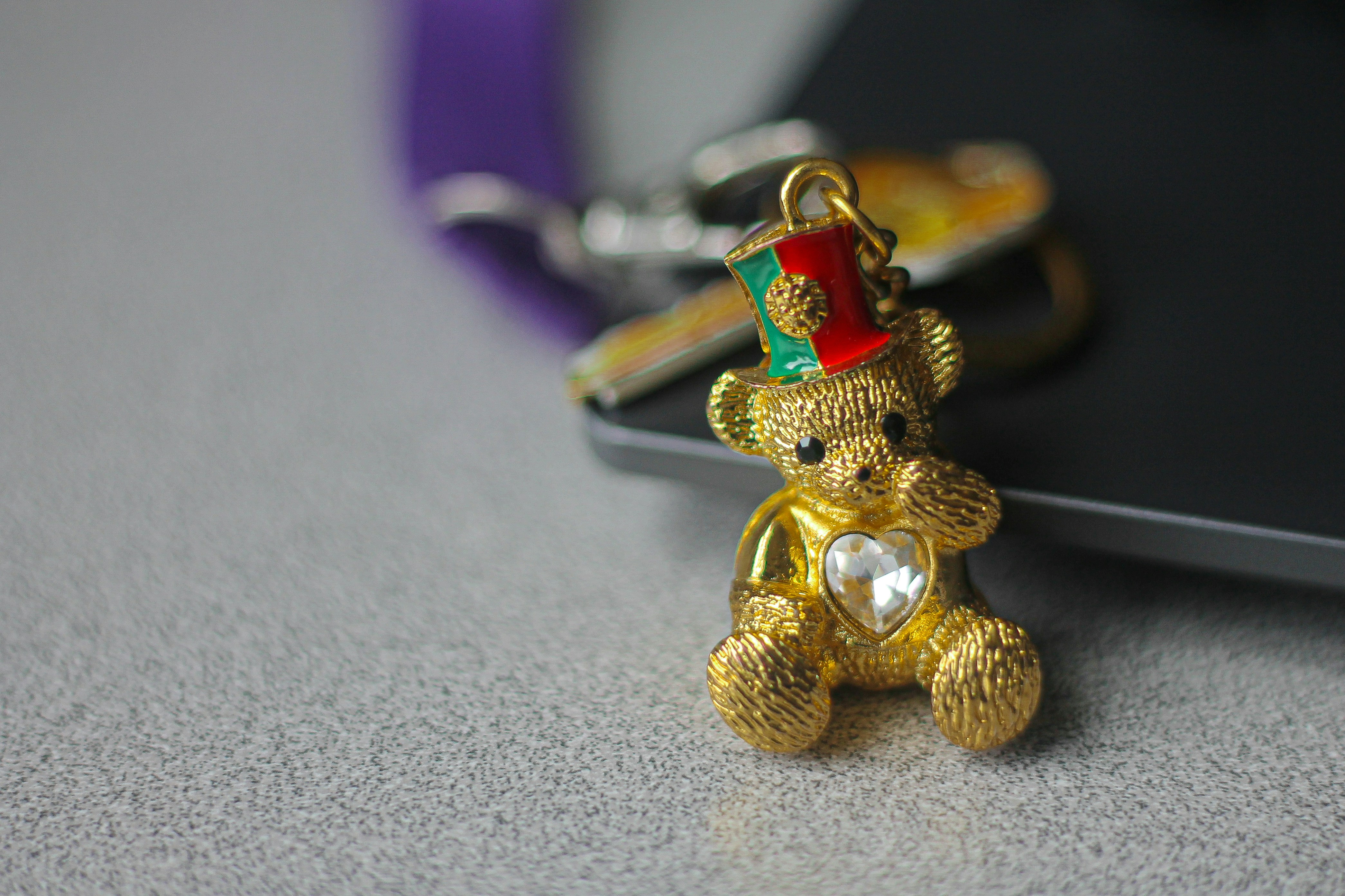Gilded Teddy Charm with Heart Gem Beside a Smartphone on a Speckled Desk