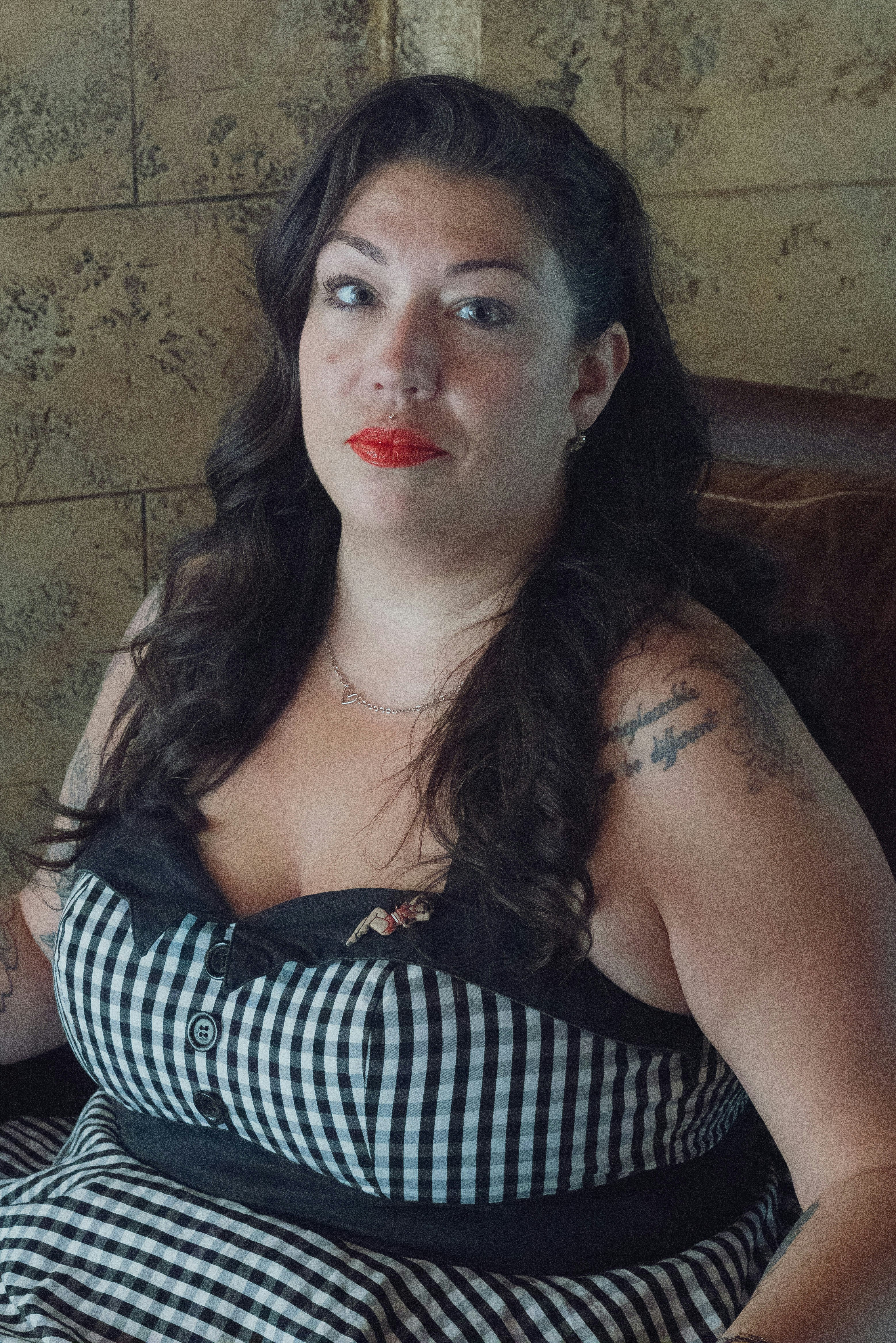 A woman with long, dark hair and red lipstick poses in a checkered dress, exuding a retro vibe against a textured backdrop.