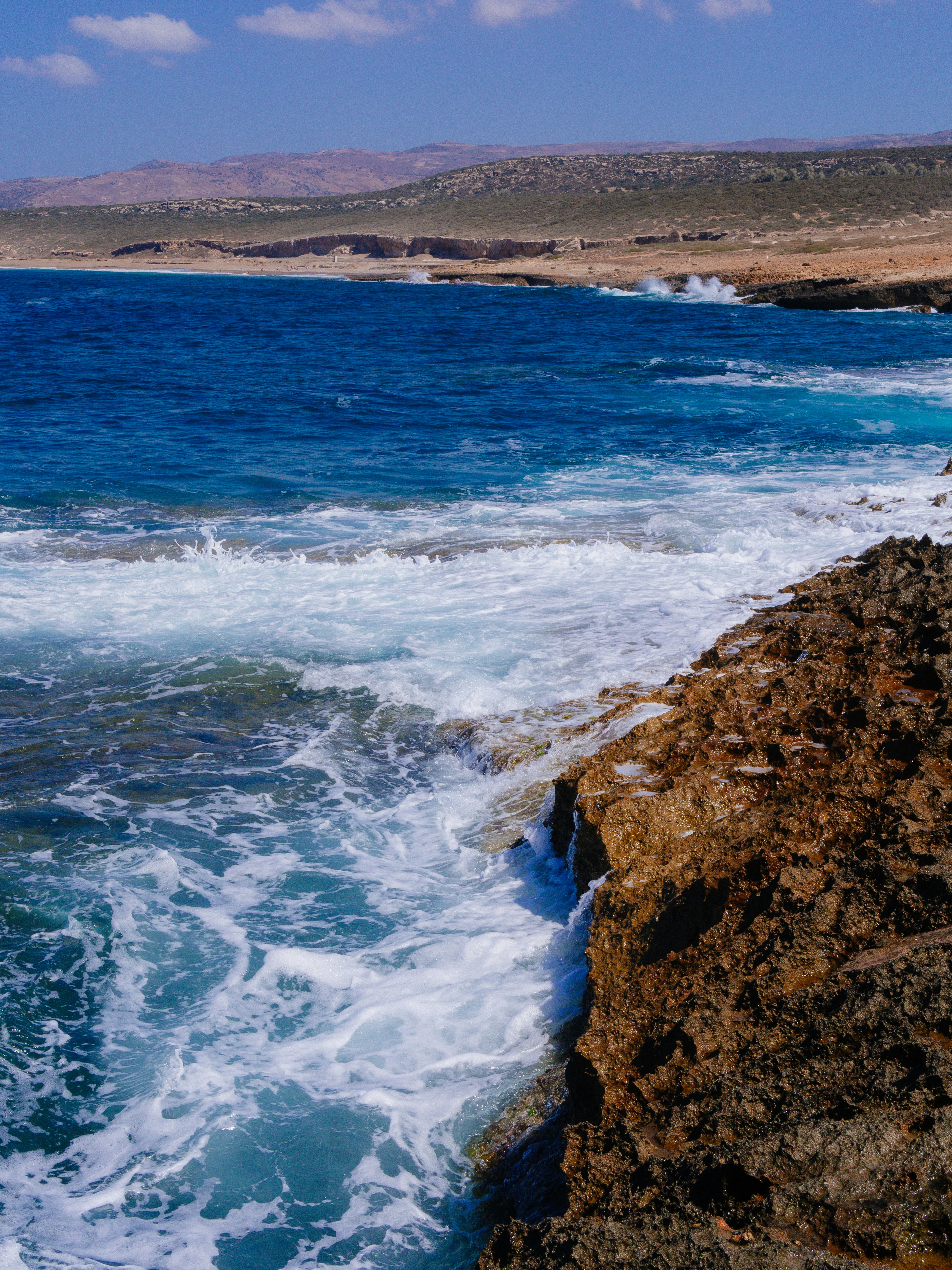Waves crash against a rocky coastline with mountains.