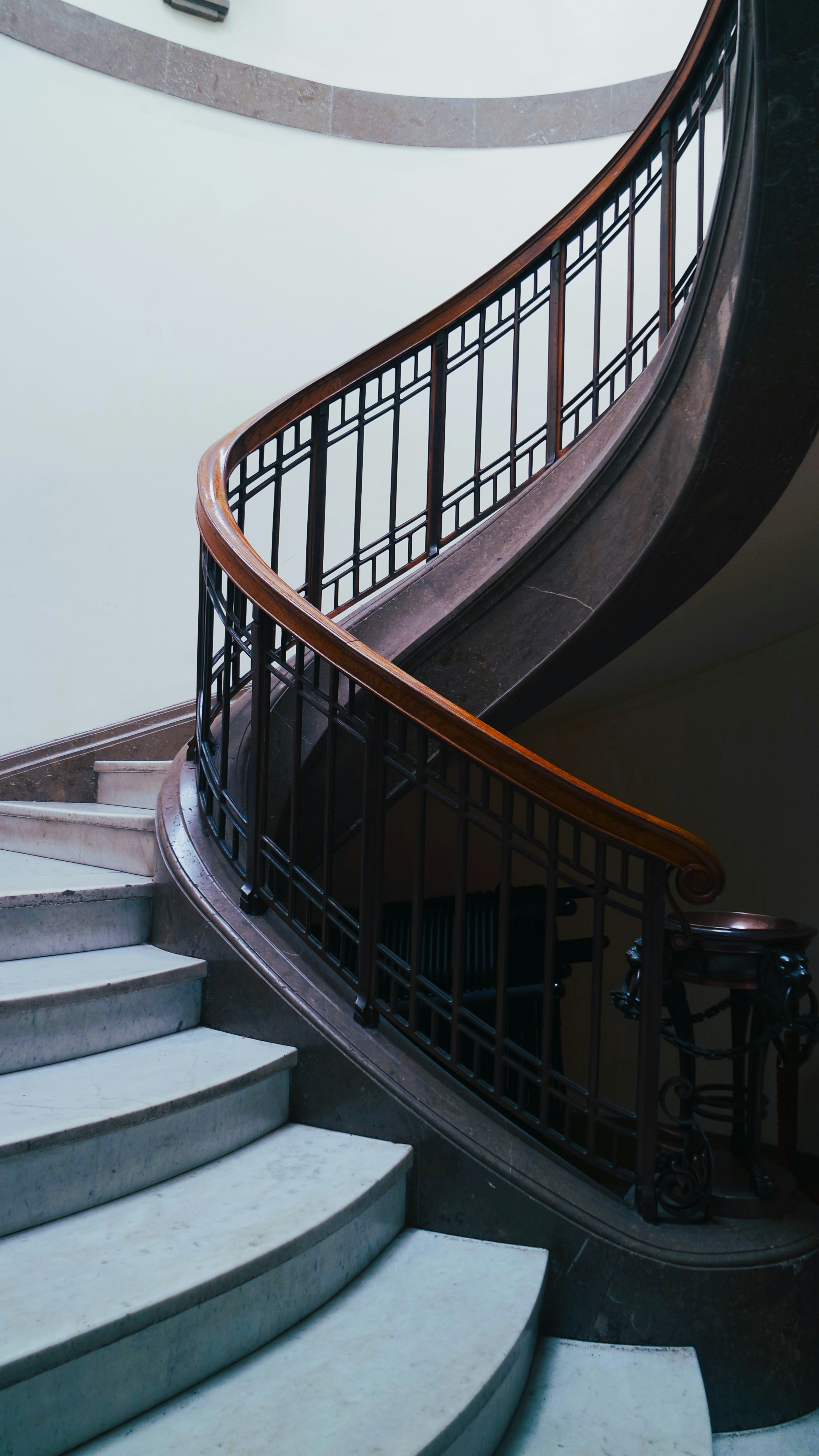 Elegant spiral staircase with a polished wooden railing and marble steps leading upward, highlighting architectural grace.