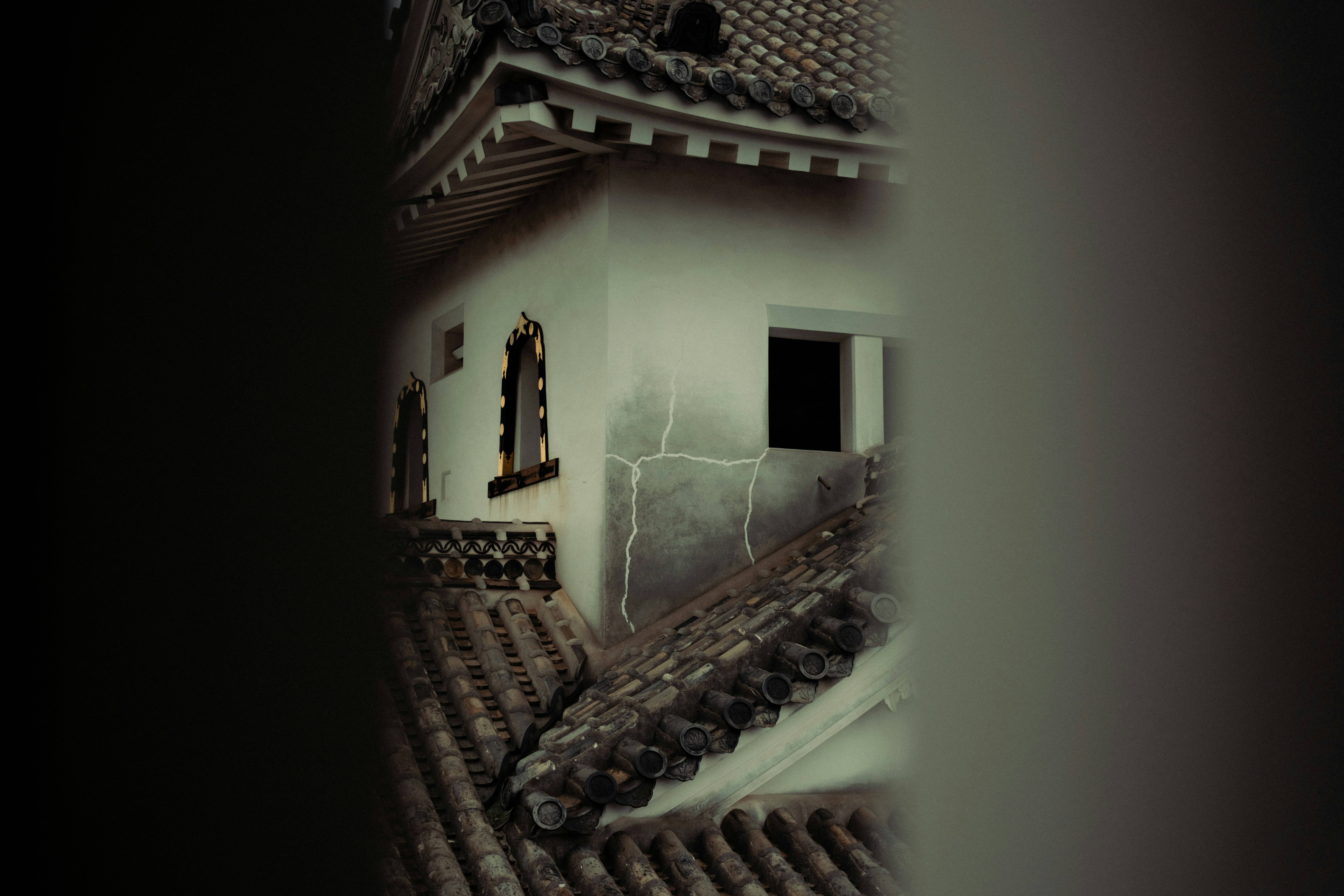 Weathered architectural details of a traditional building, framed by a narrow opening. The interplay of light and shadow highlights the textures of the roof and walls.