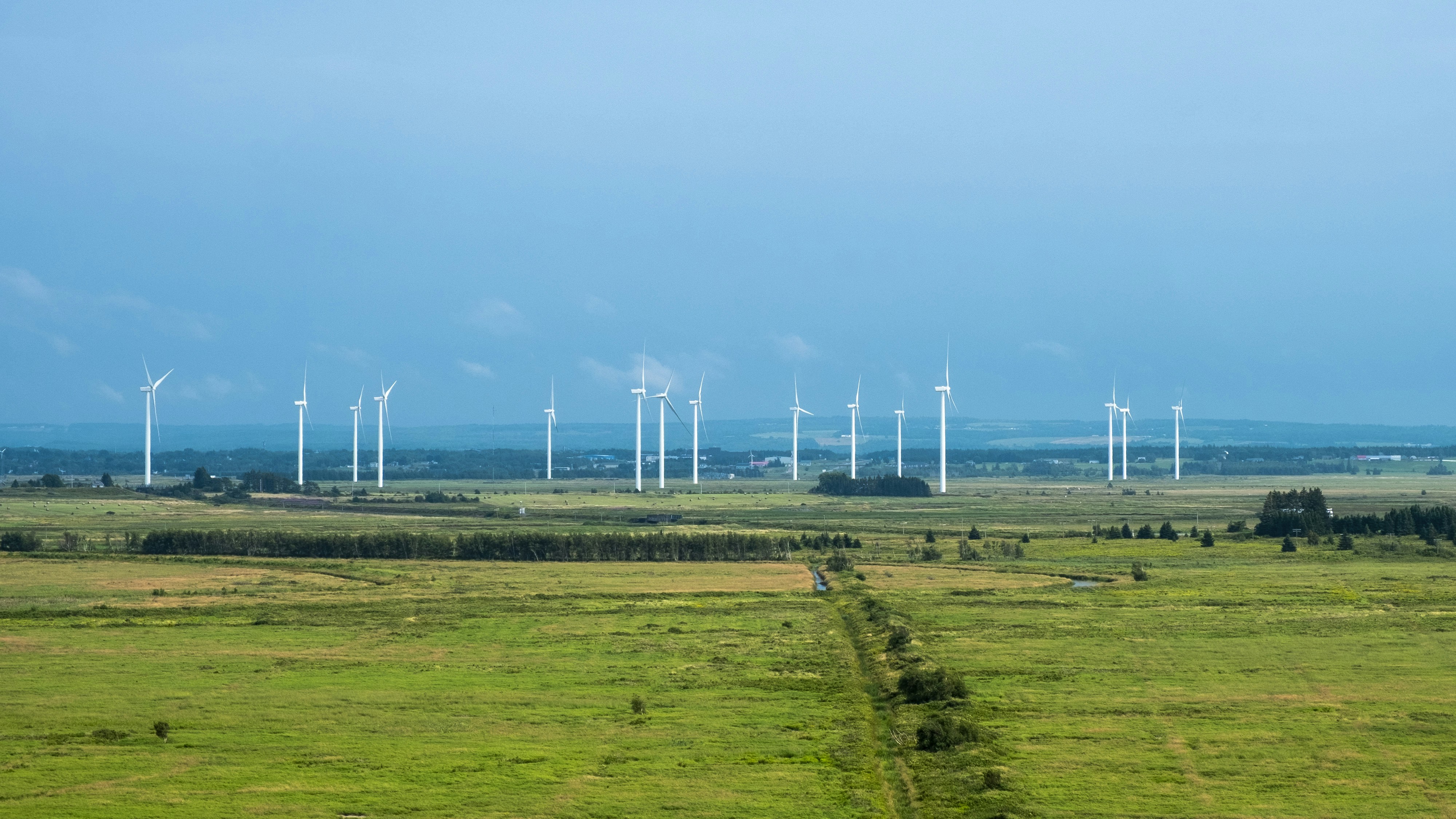Wind turbines stand in a green field under a blue sky.