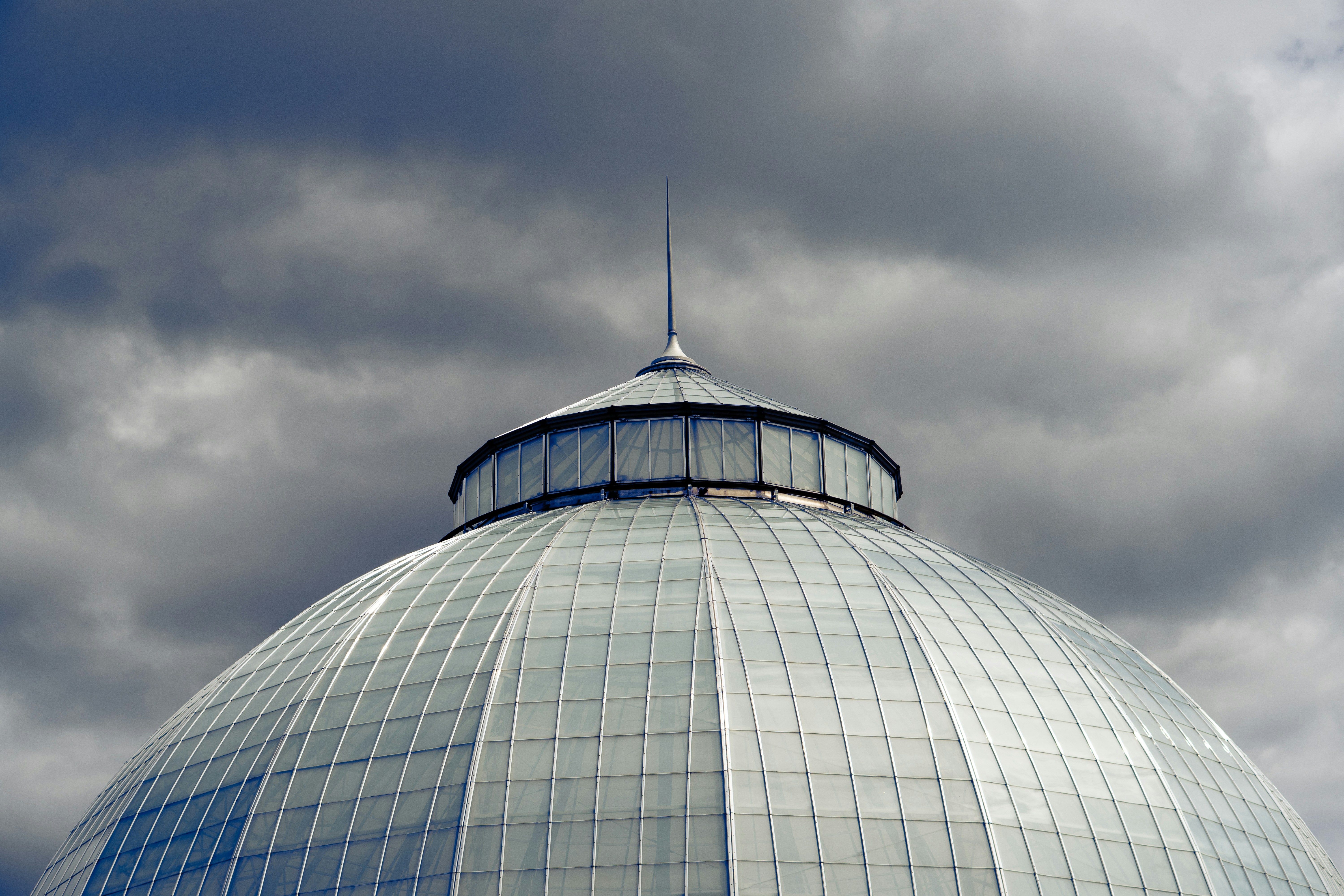 A close-up view of a glass dome structure under a dramatic sky, showcasing its intricate design and reflective surfaces.