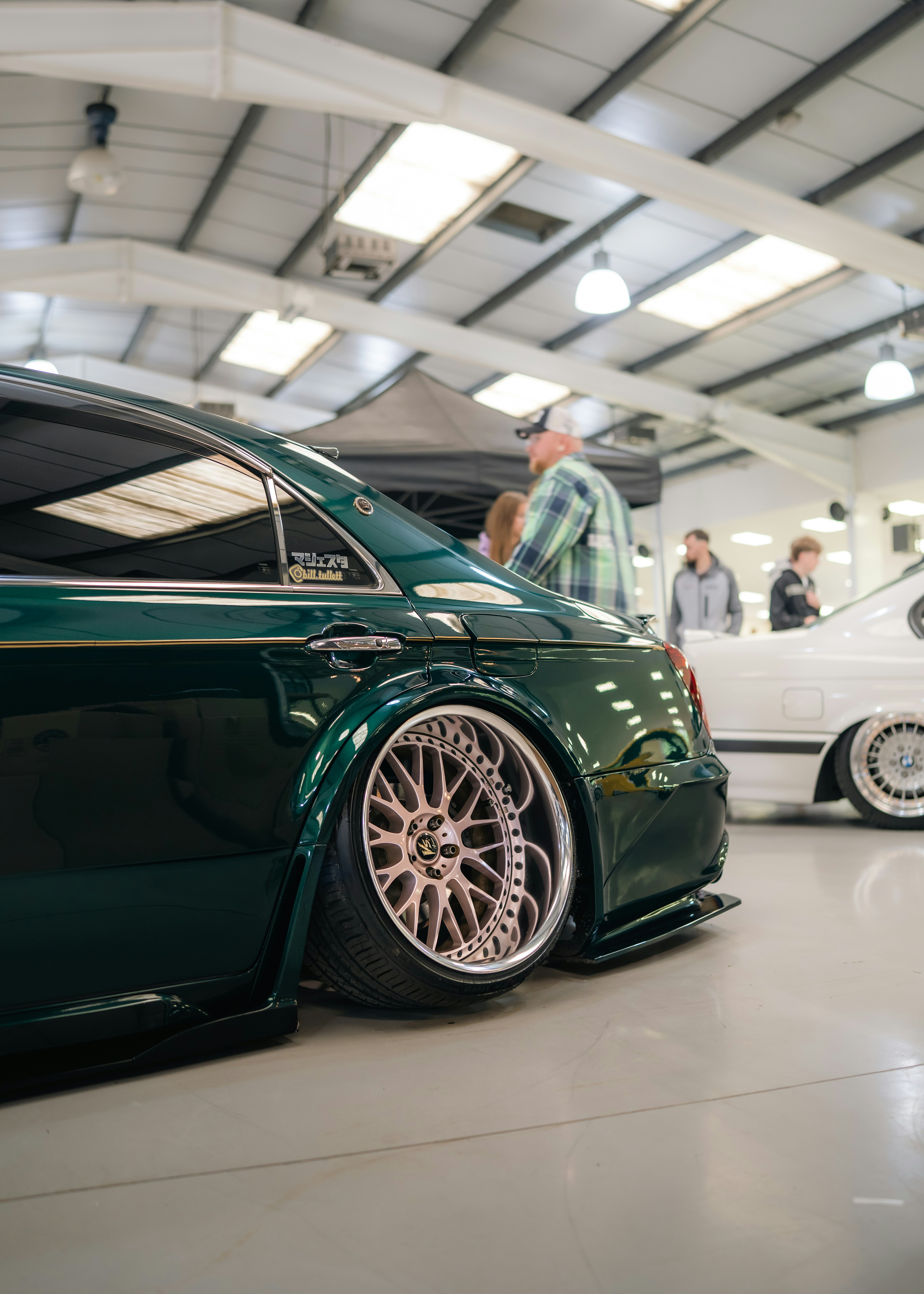 Modified luxury car showcasing a gleaming green finish and intricate alloy wheels in a well-lit exhibition space.