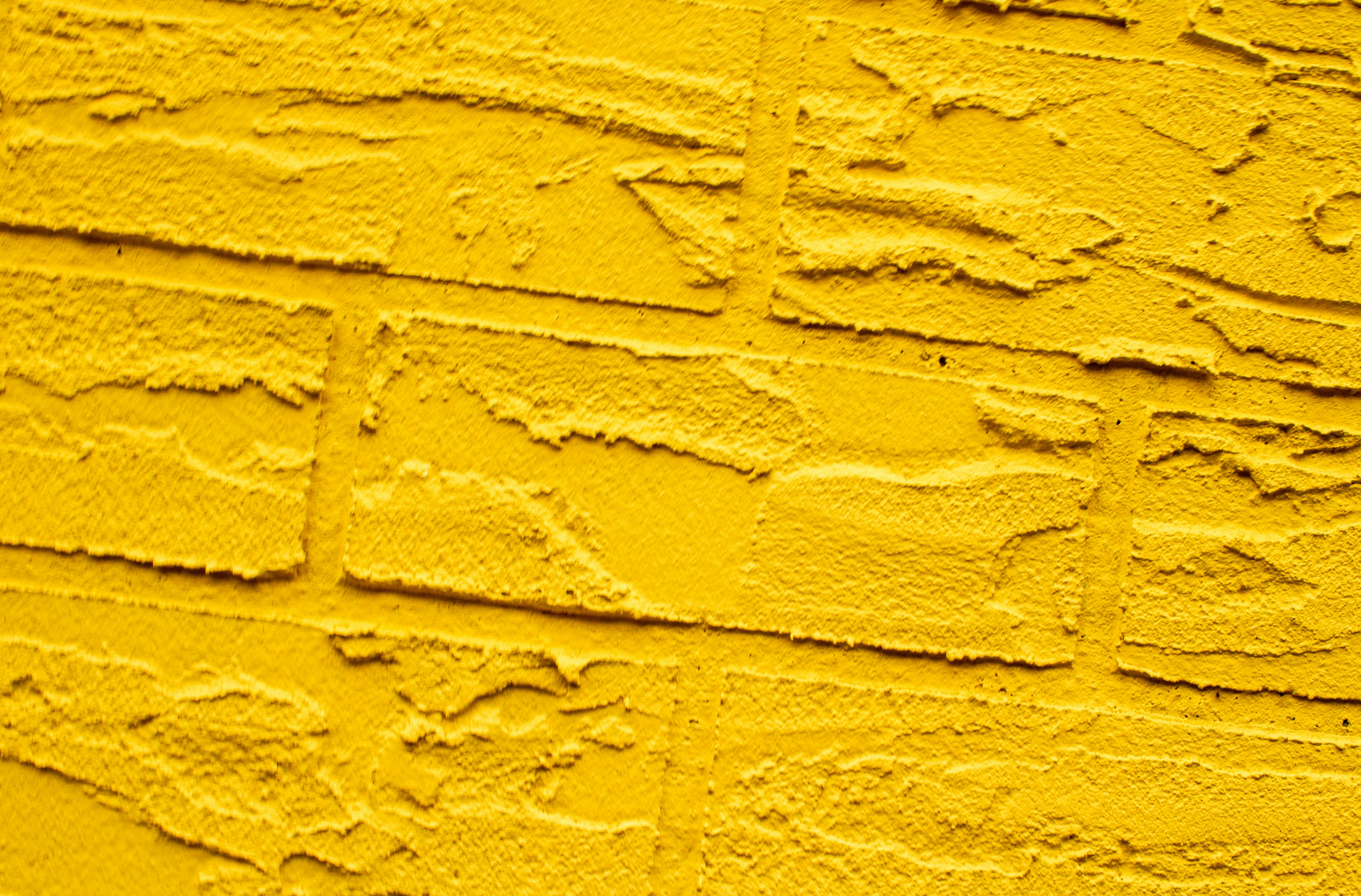 A close-up view of a bright yellow textured wall. The vivid color and tactile quality create a striking visual that serves as an ideal backdrop for design, branding, or architectural themes. The surface features deliberate ridges and indentations, offering depth and contrast. Common in urban environments, such walls are often used to create a bold visual identity or highlight specific design zones. The strong hue and distinct texture enhance its visual appeal for creative use.
