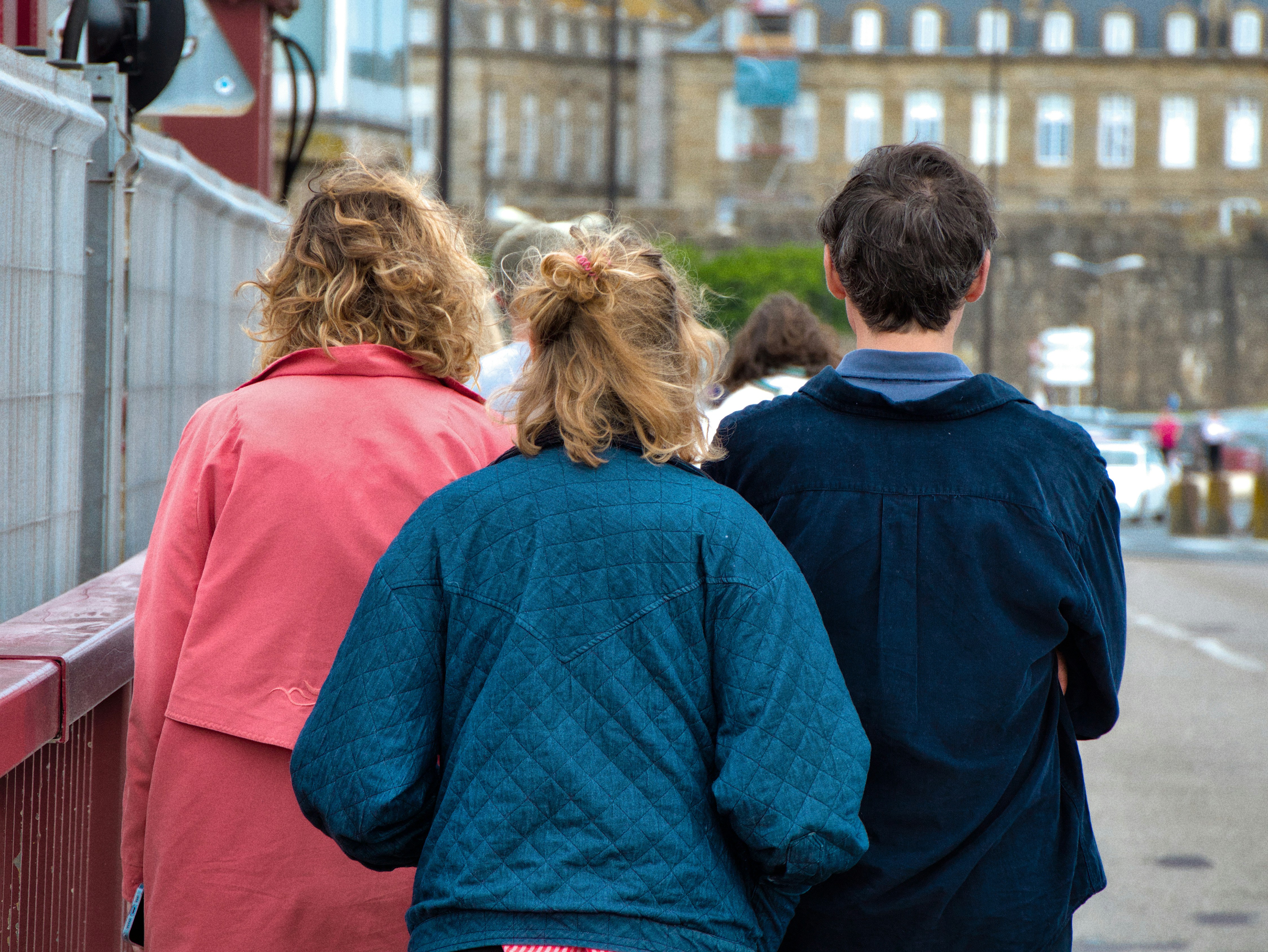 Three individuals walking side by side along a city street, showcasing a blend of colorful jackets and a casual atmosphere.