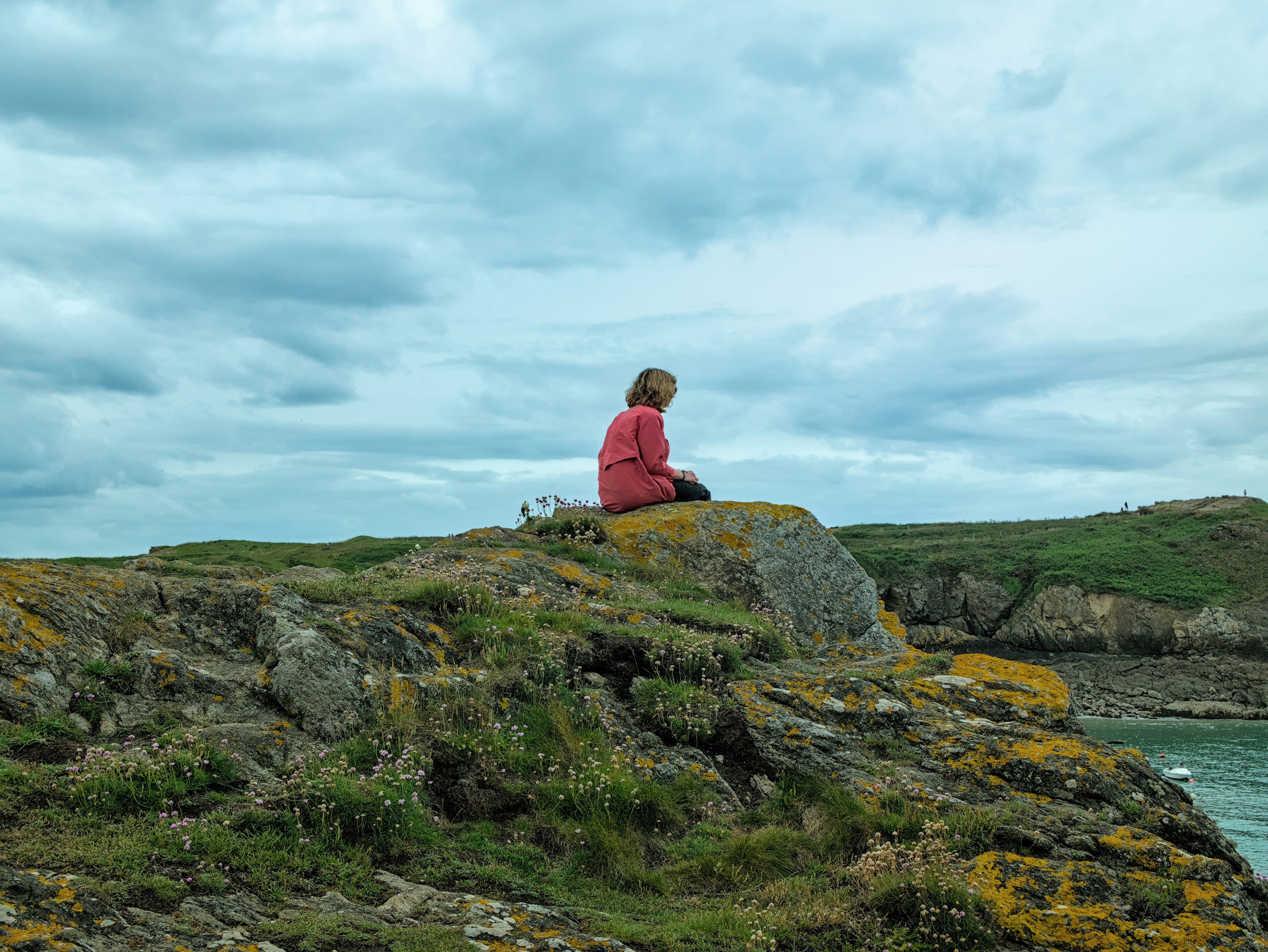 lone woman sitting on a rock near the sea, on a peaceful coast, under a cloudy sky