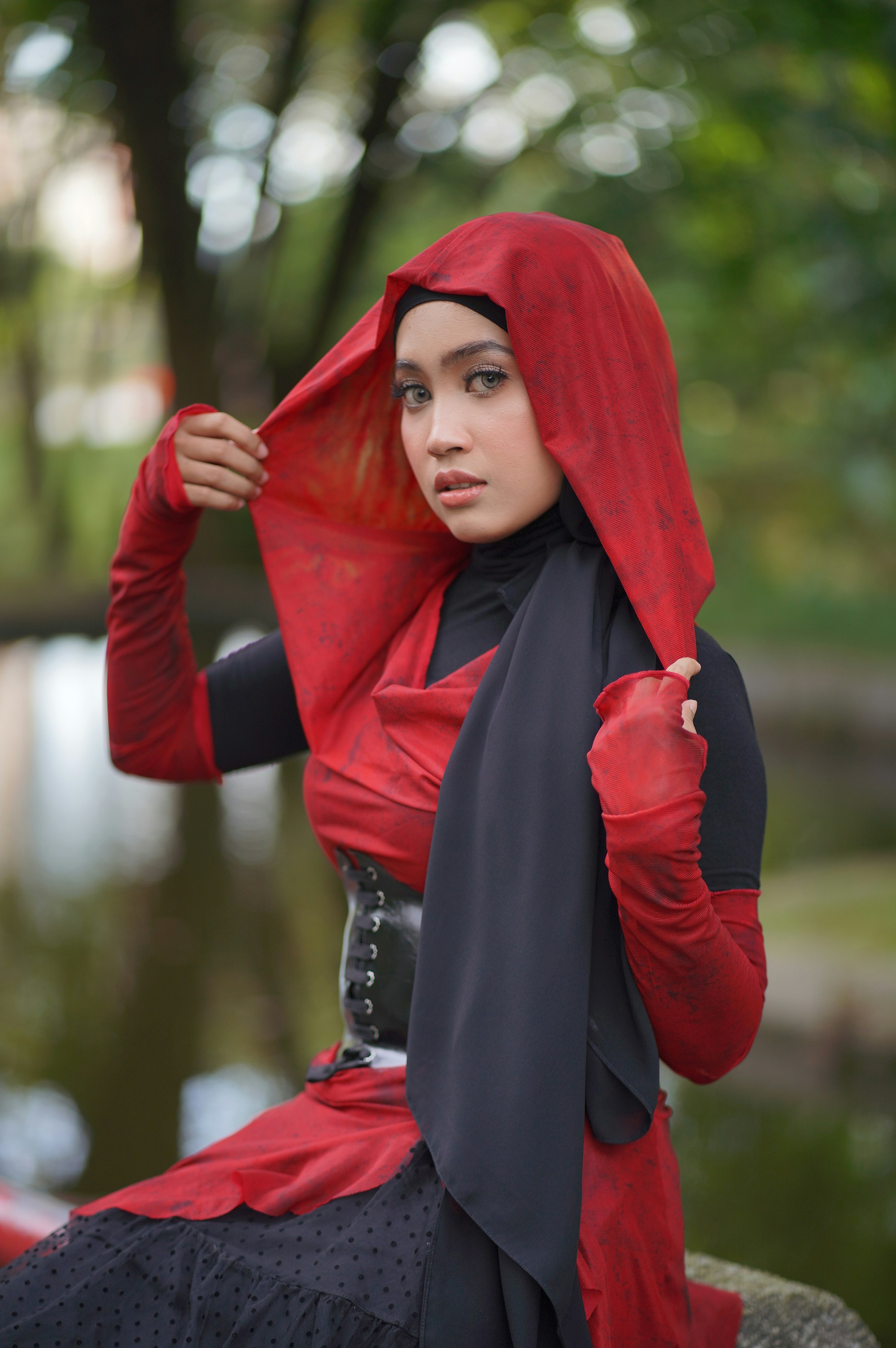 Woman in red hood poses elegantly outdoors.