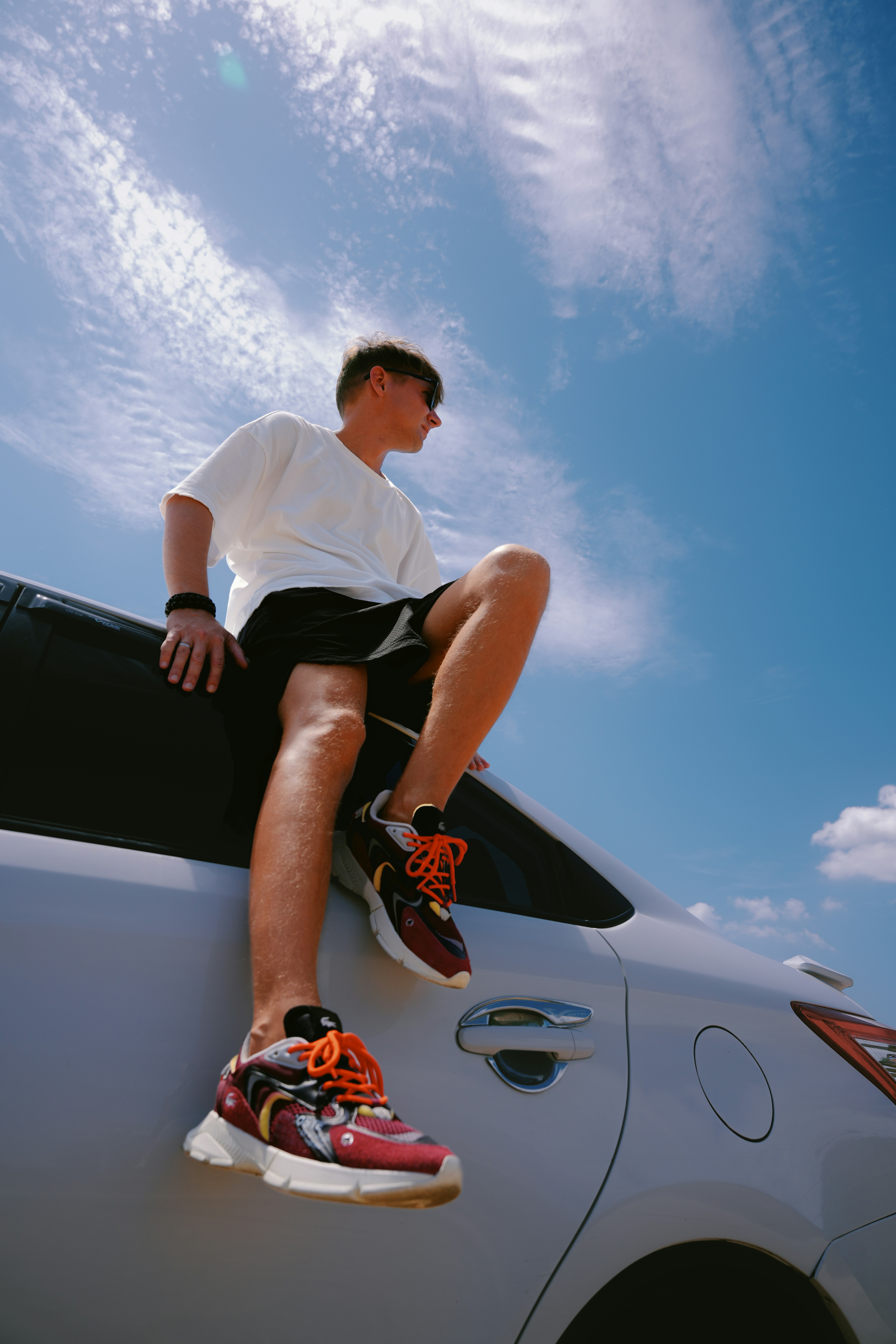 Sunlit Summit: A Man Perched on a White Sedan Beneath a Vast Blue Sky