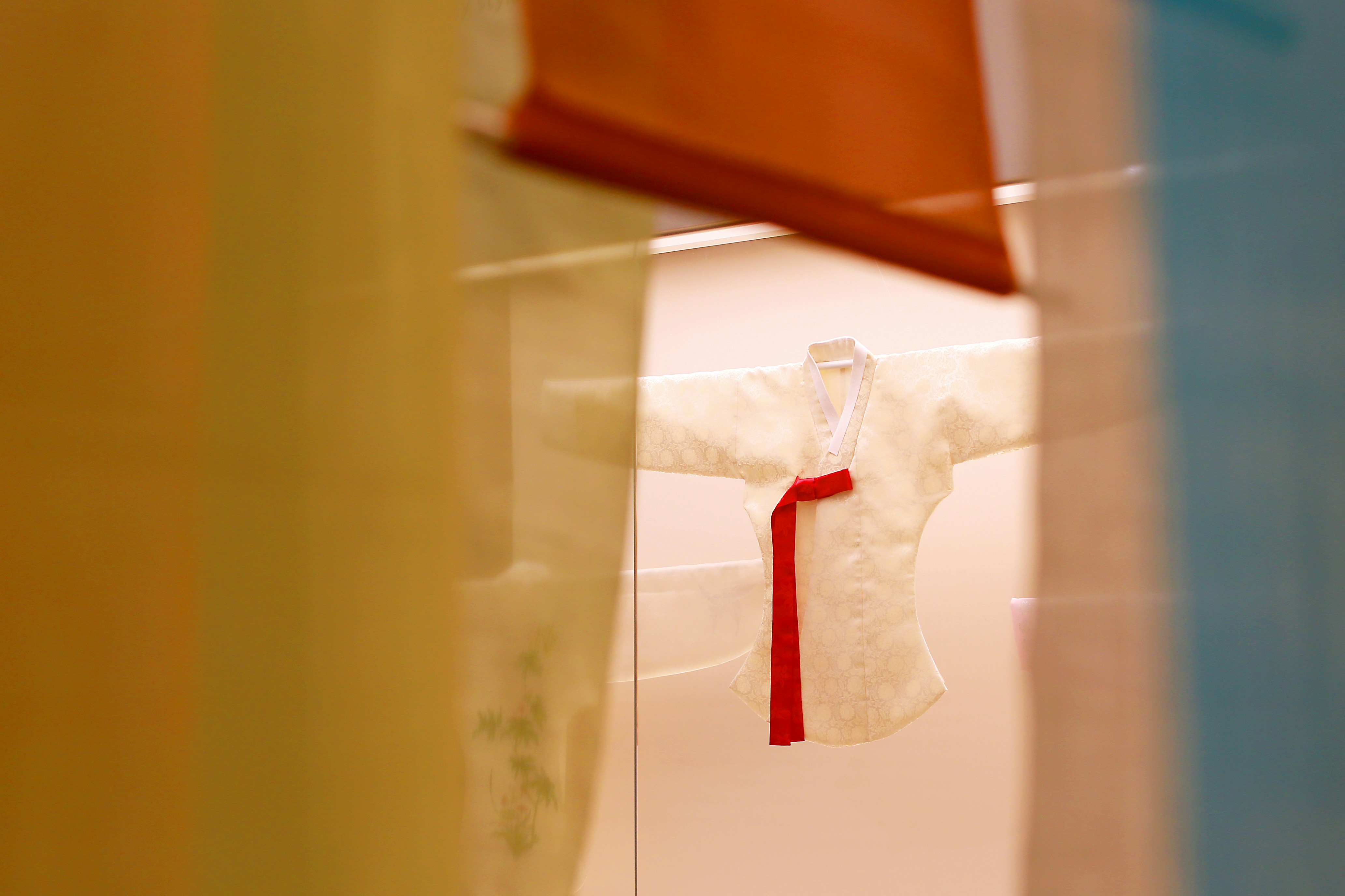 Traditional garment with a red ribbon displayed behind colorful translucent panels.