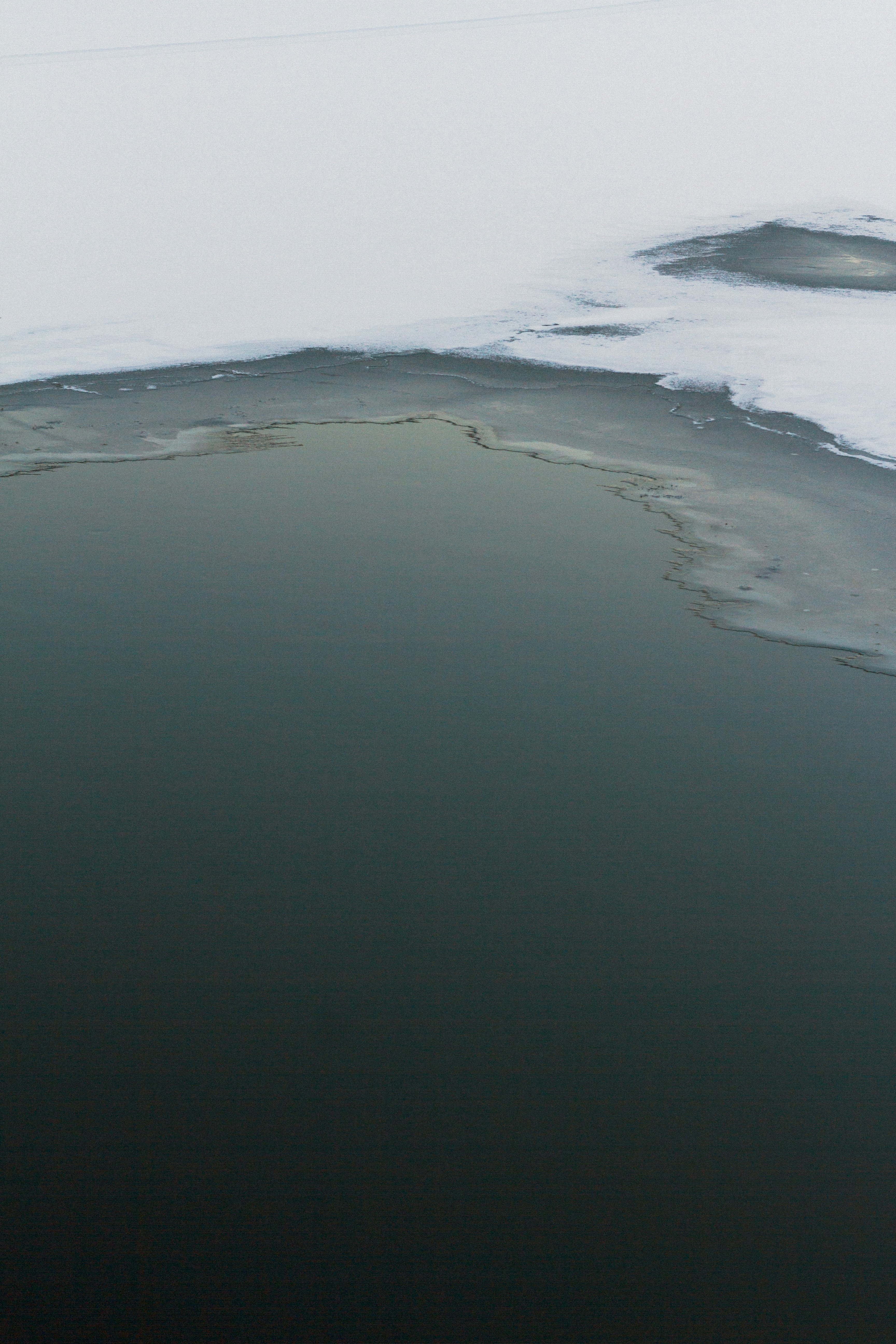 Dark water meets icy shoreline, capturing the transition between solid and liquid in a serene winter landscape.