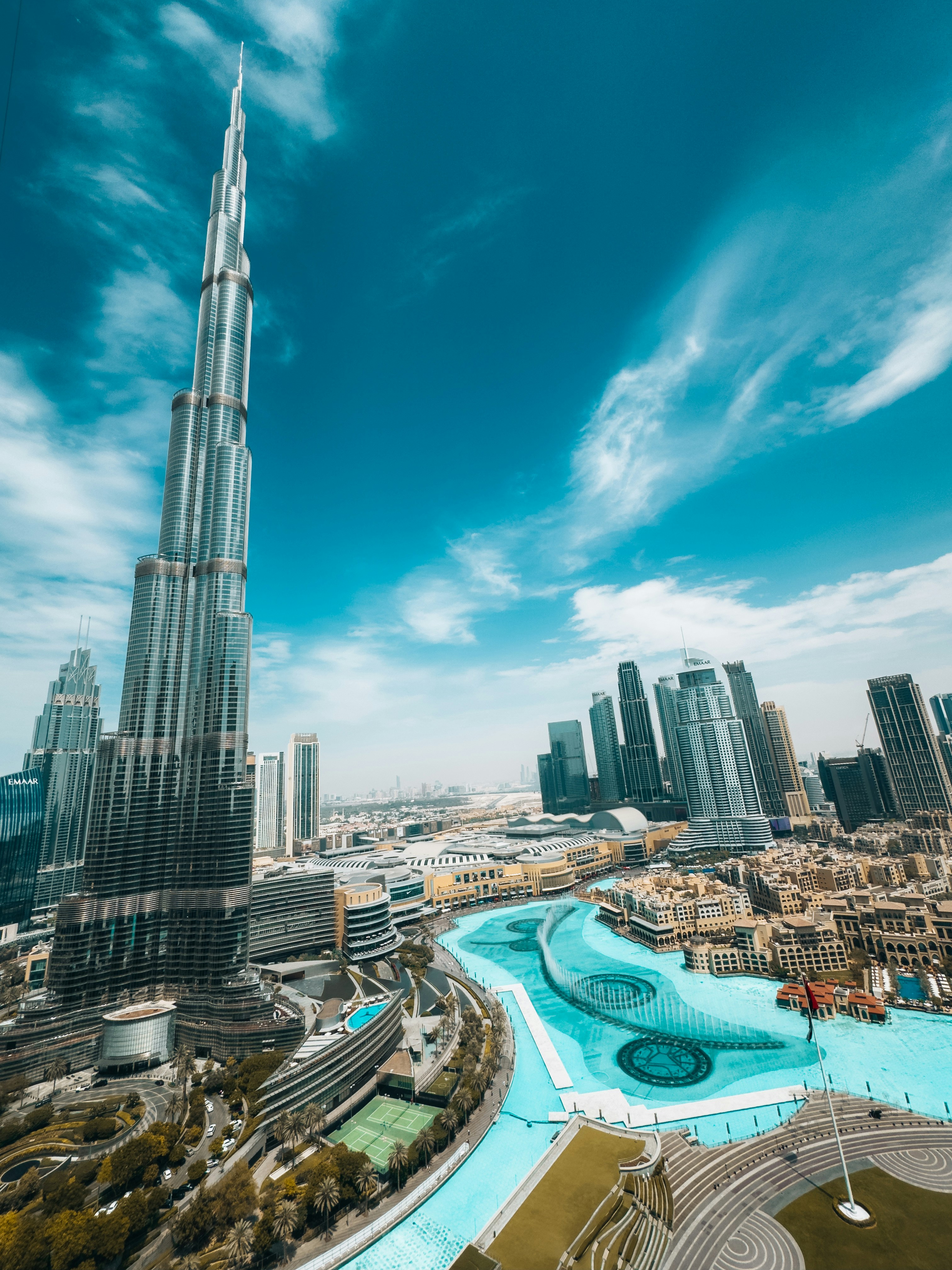 Burj Khalifa towers over a vibrant cityscape, with a winding waterway and modern architecture below. Bright blue skies enhance the scene.