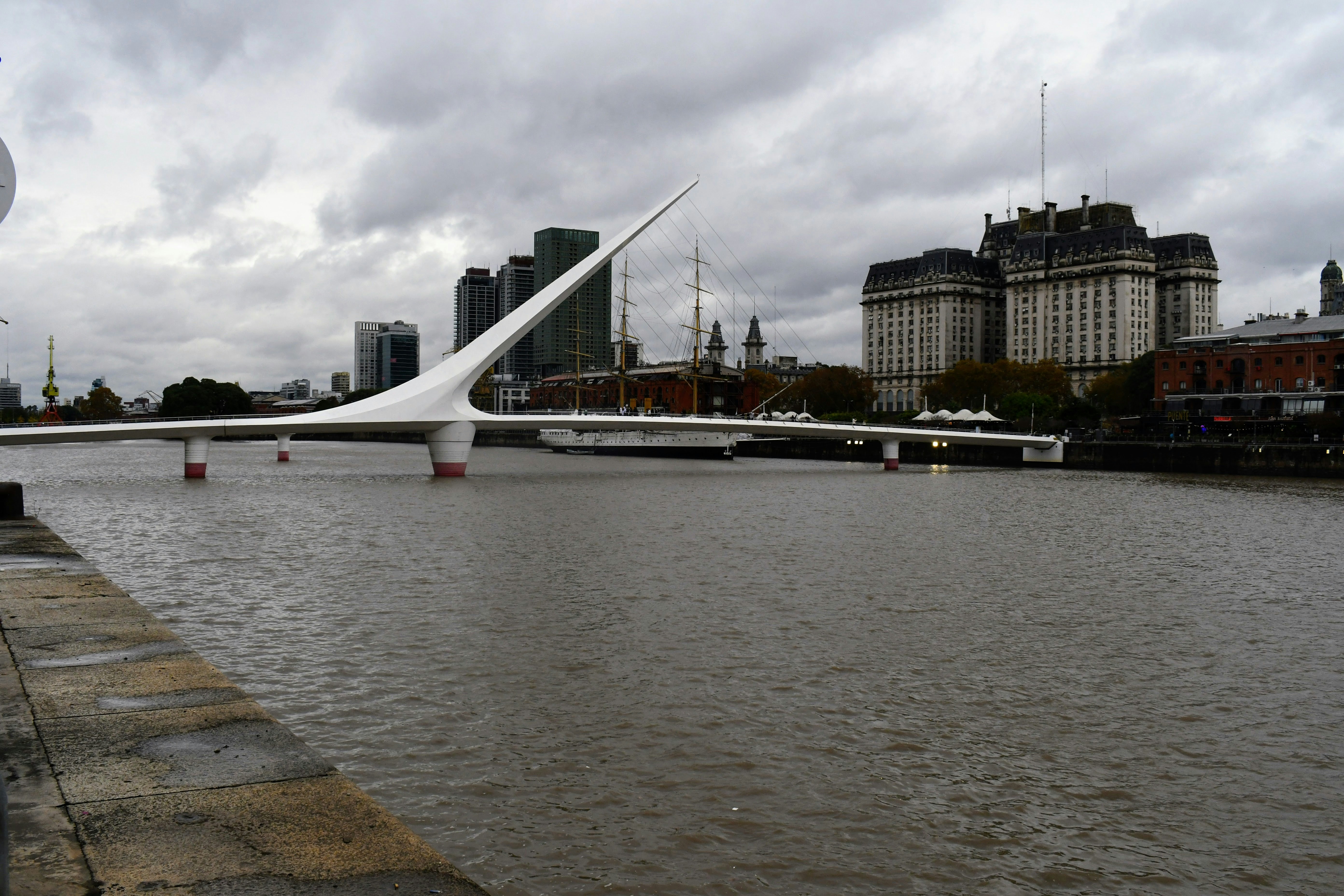 Sculpted Arc over the Thames: a modern bridge slicing through a clouded cityscape.