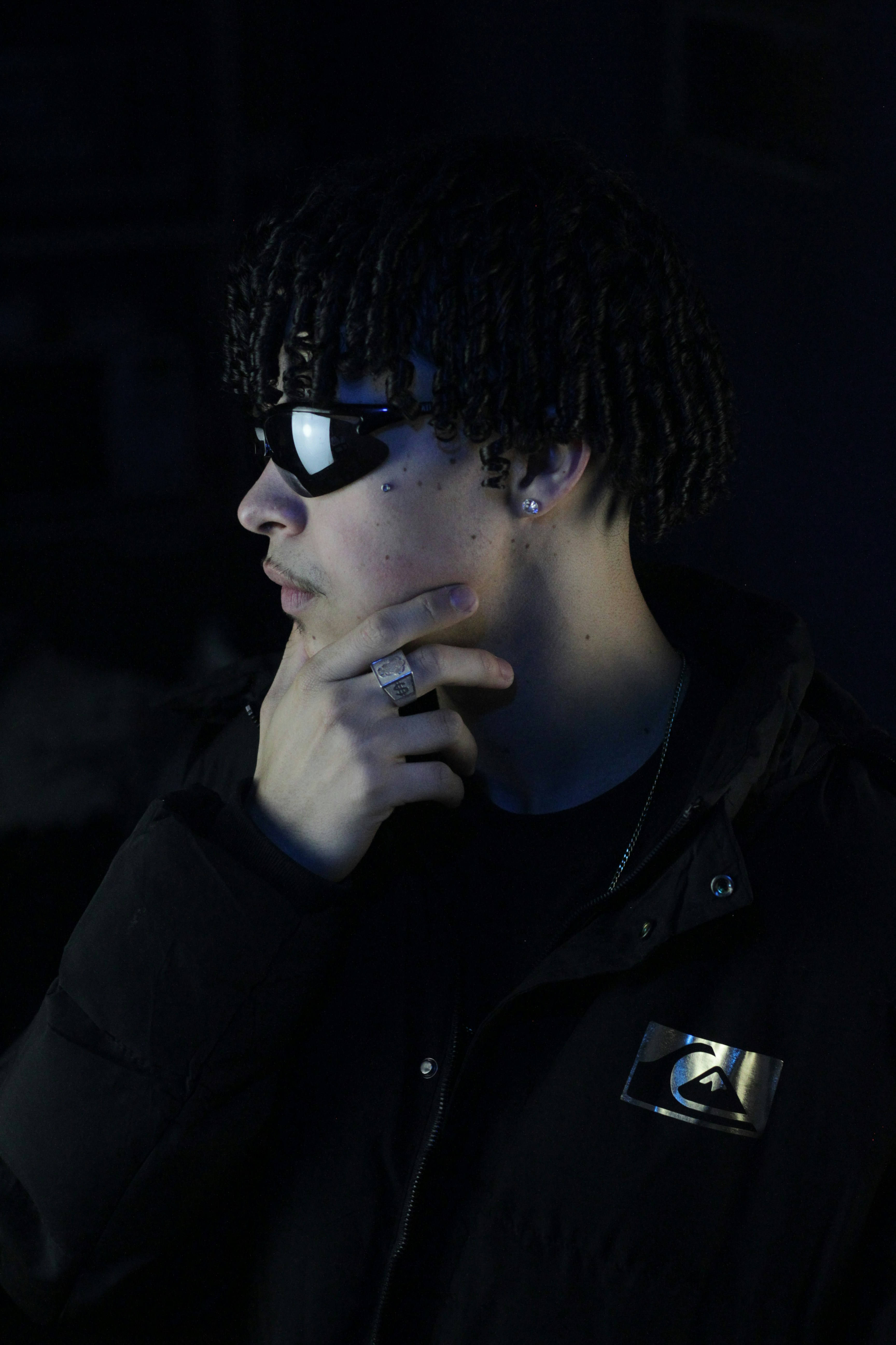 A young man poses in sunglasses and jacket.