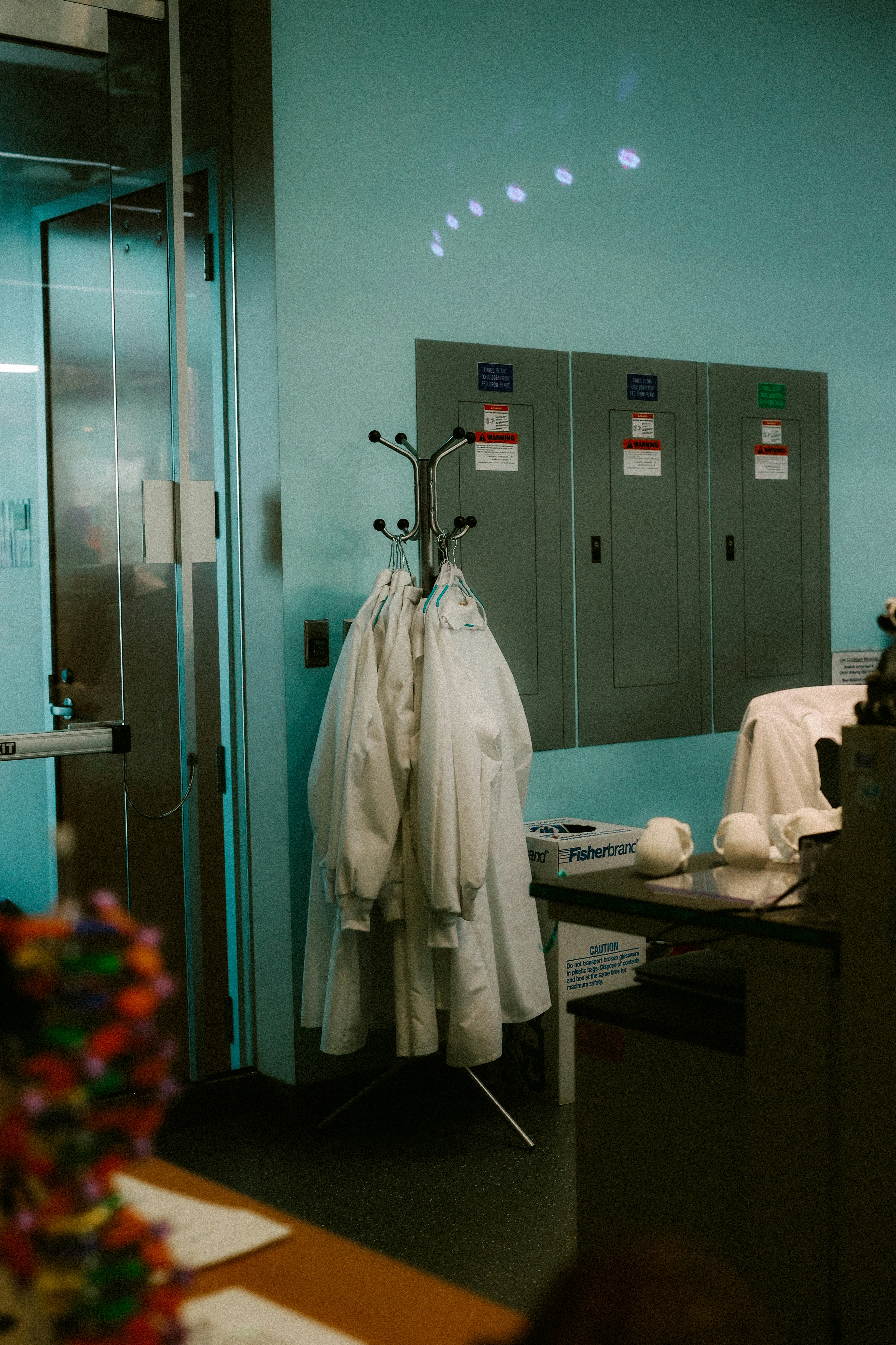 Teal-Walled Prep Room: White Lab Coats on a Stand by Grey Lockers