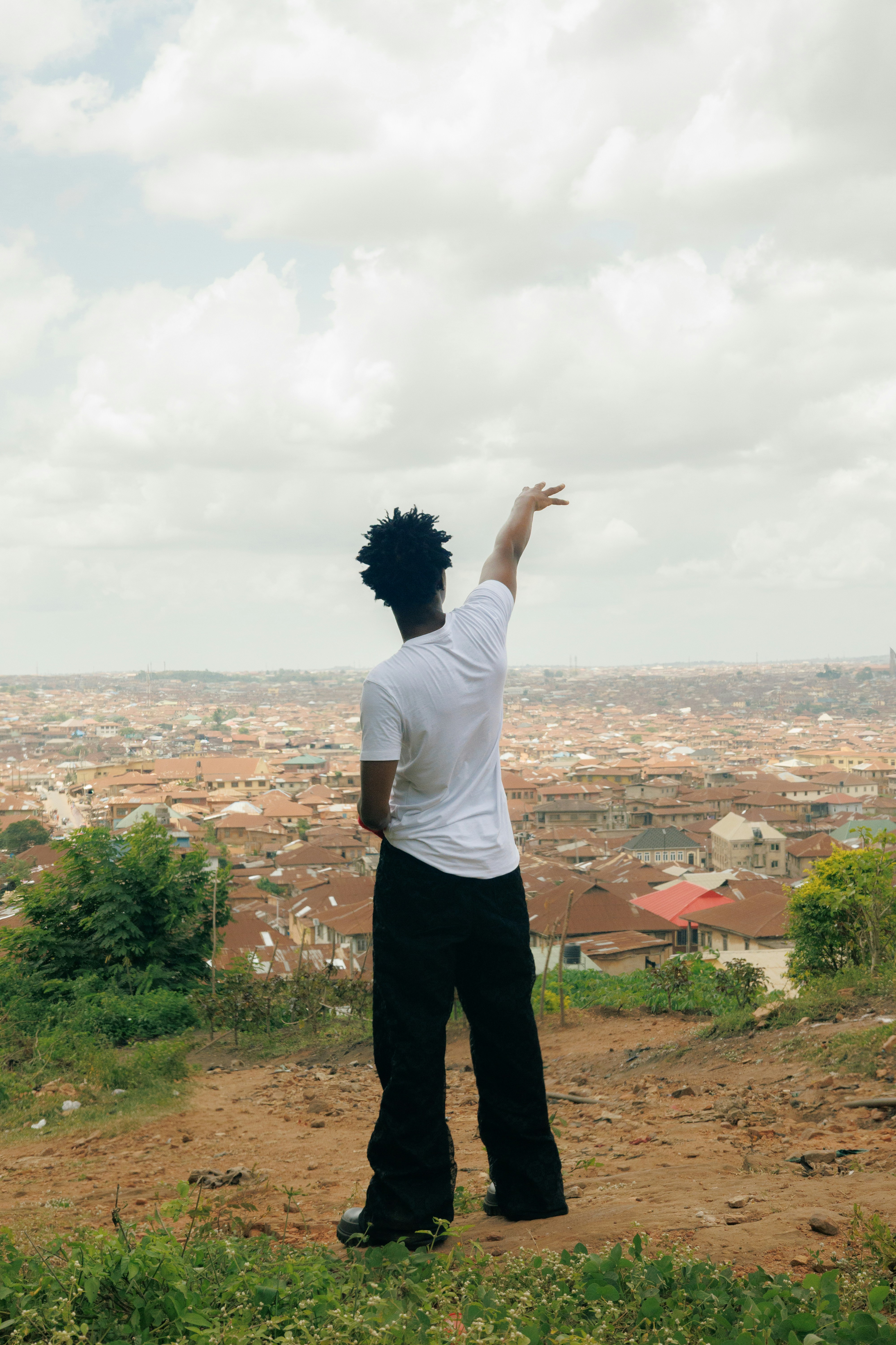Horizon Hand Raised: A lone figure surveys a sea of terracotta rooftops from a hillside overlook