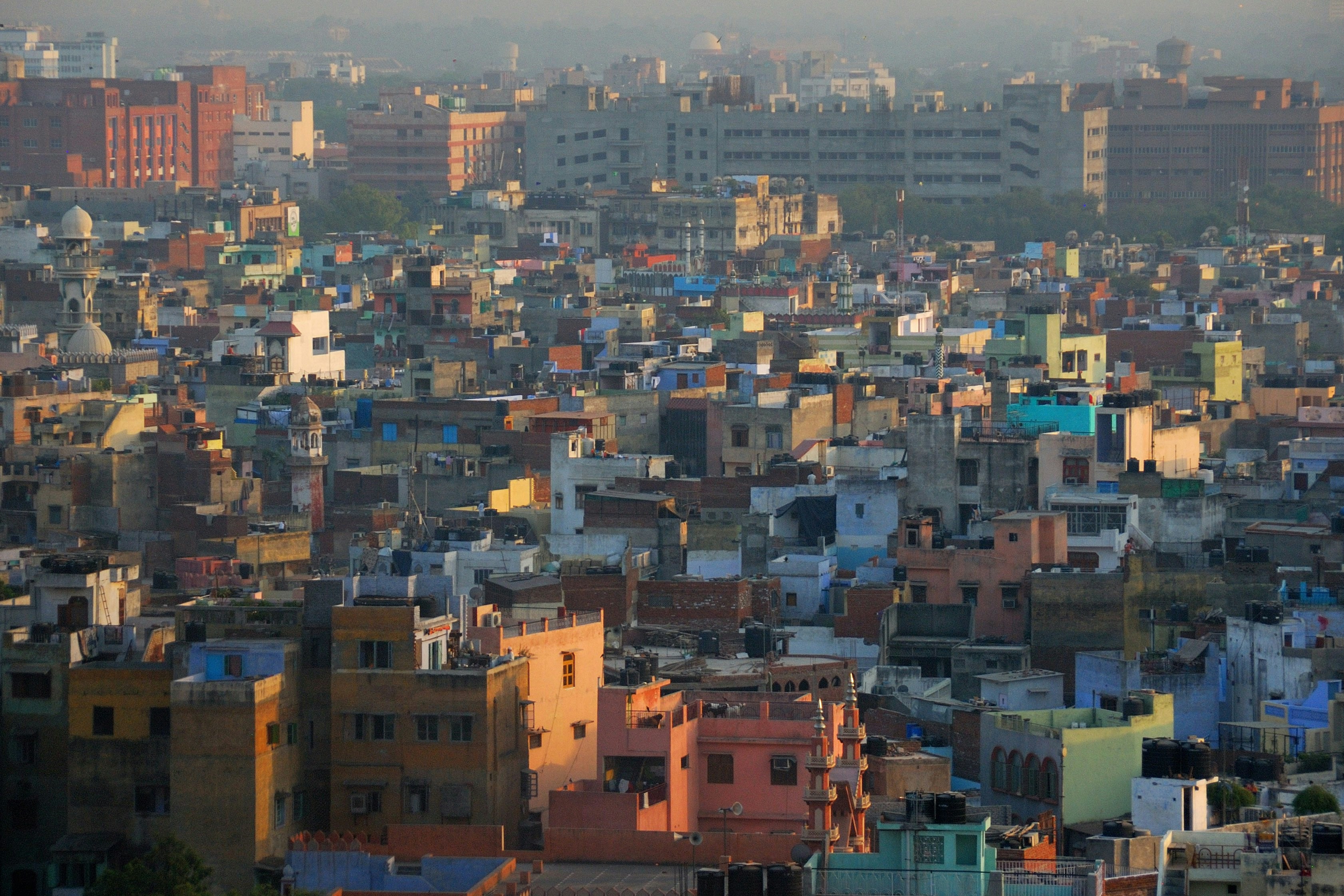 Vibrant rooftops of densely packed buildings create a patchwork of colors in a bustling urban landscape. The scene captures the essence of city life.