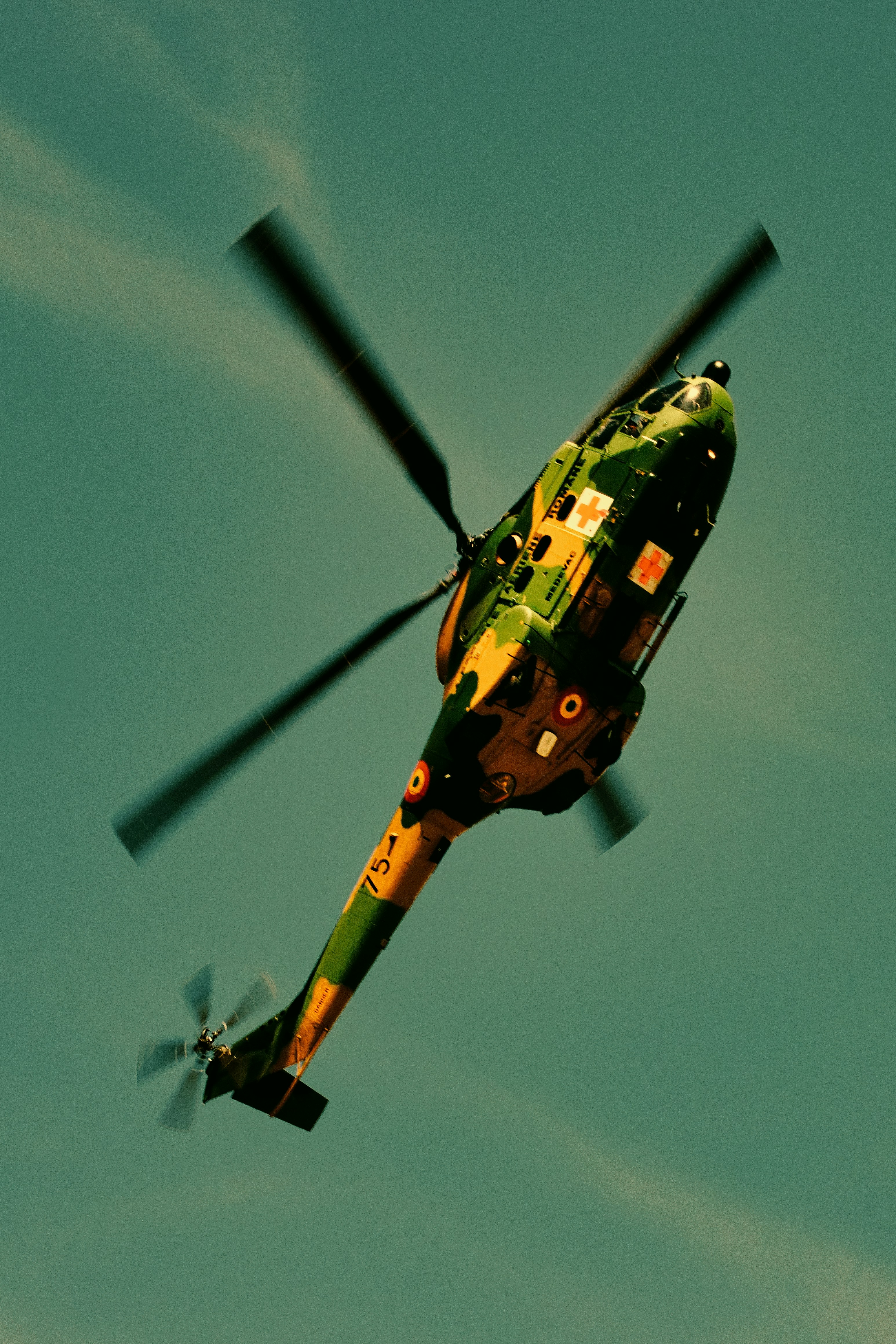 Tilted Rescue: Camouflaged helicopter carving through a pale sky