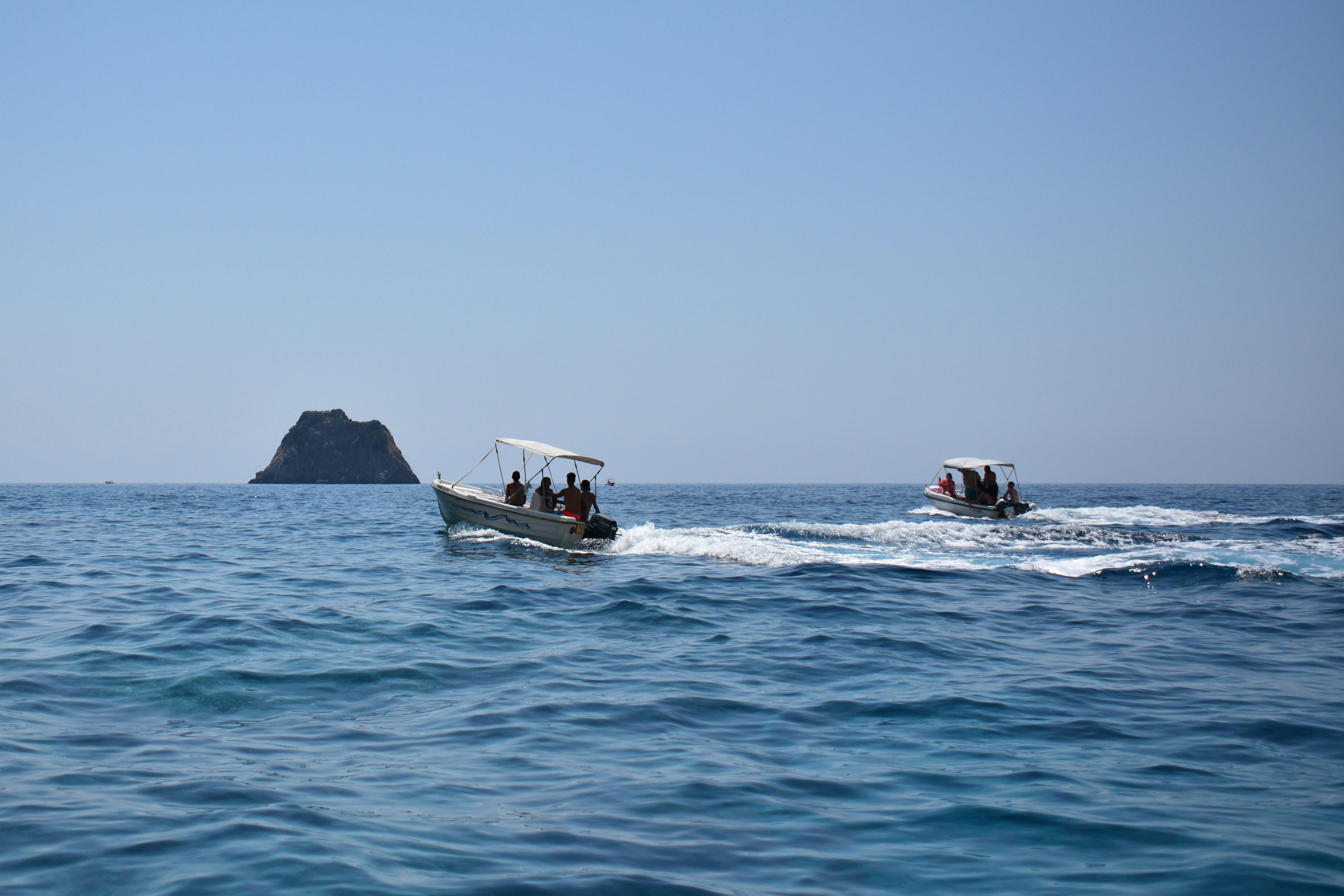 Twin Boats Skim the Blue Wake Toward a Distant Rock Island