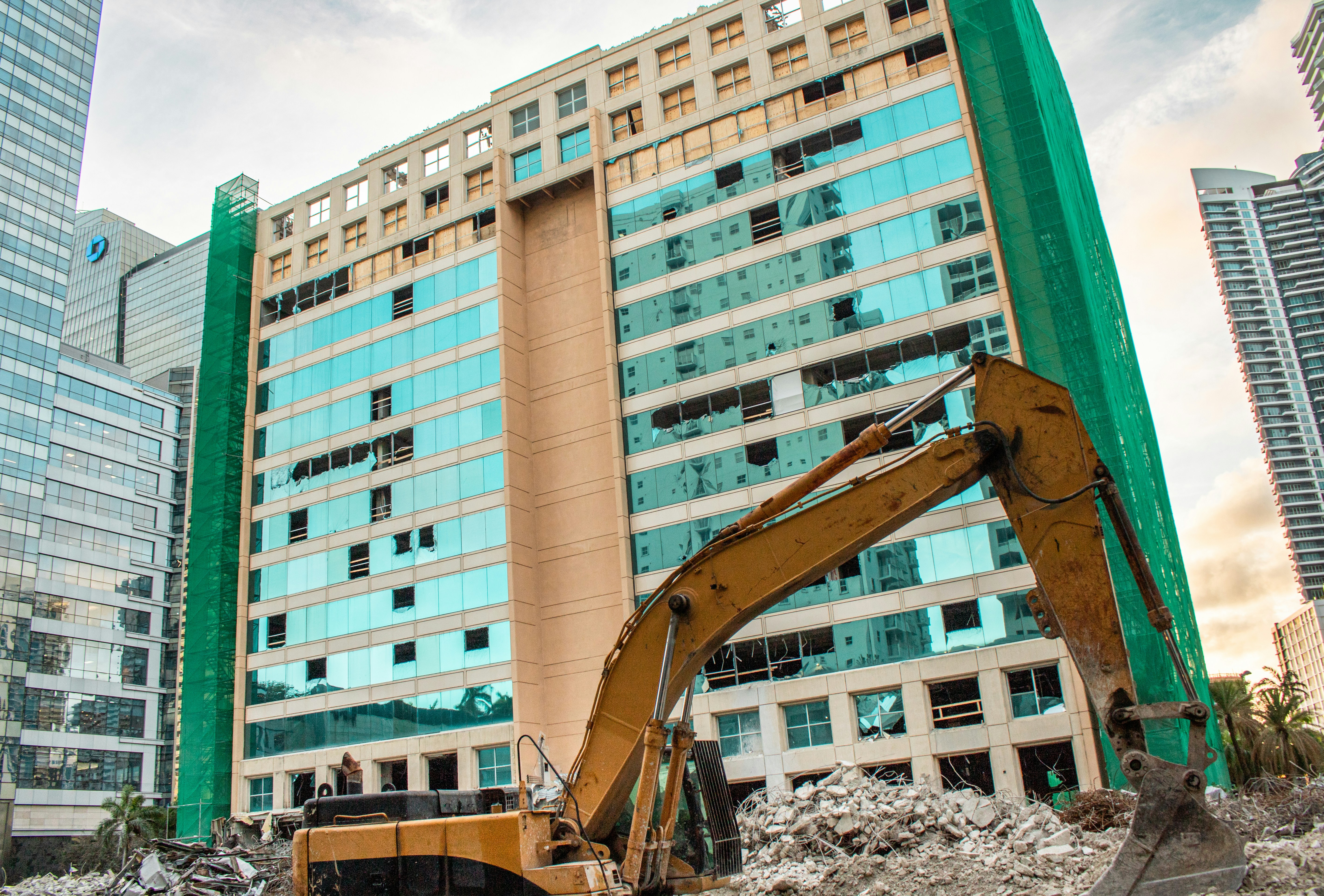 Construction machinery at work in front of a partially demolished building, showcasing the transition of urban landscapes. Green scaffolding hints at future developments.