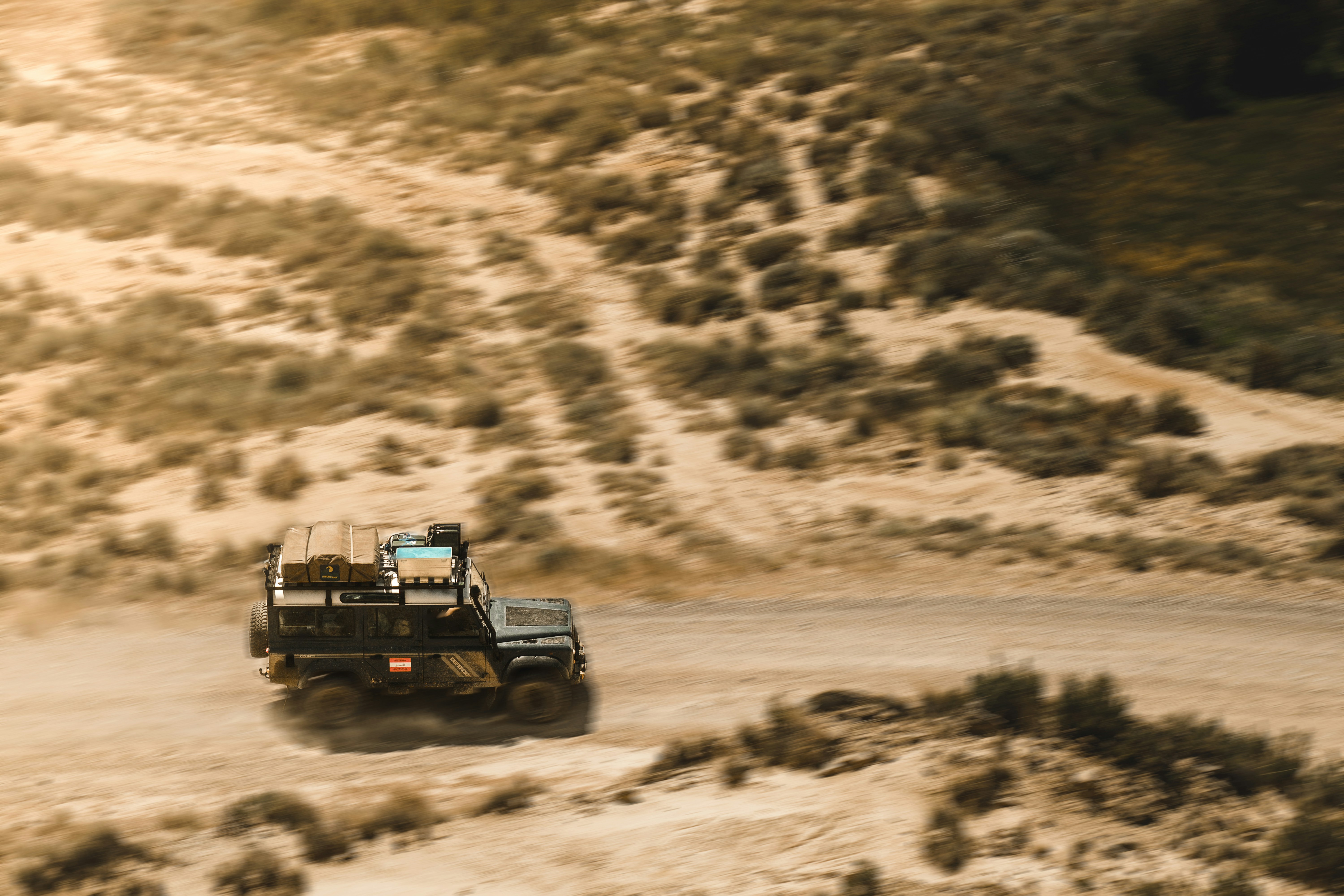 Off-road vehicle navigating a rugged desert terrain under golden sunlight.