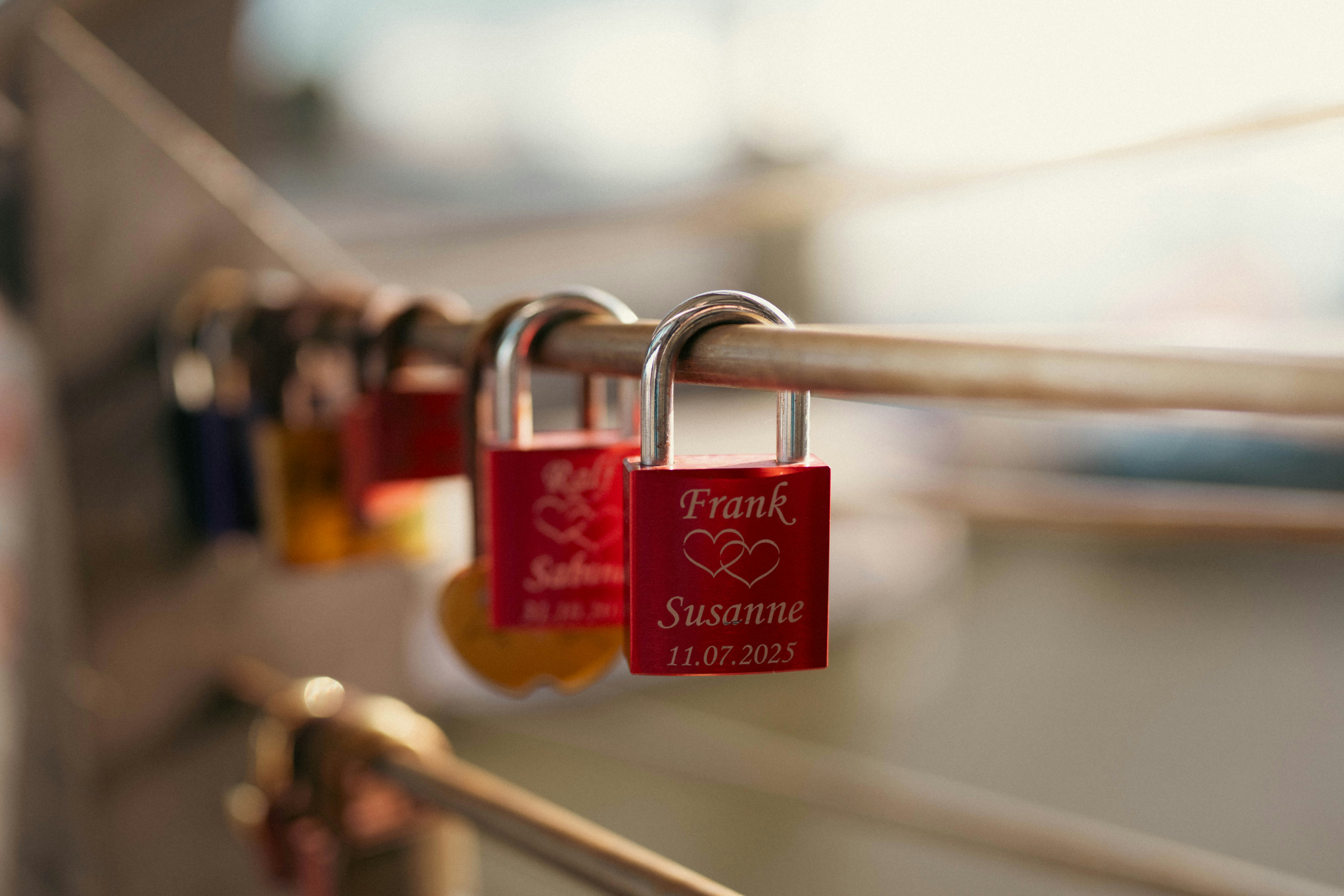 Colorful padlocks inscribed with names and dates hang on a railing, symbolizing love and commitment.