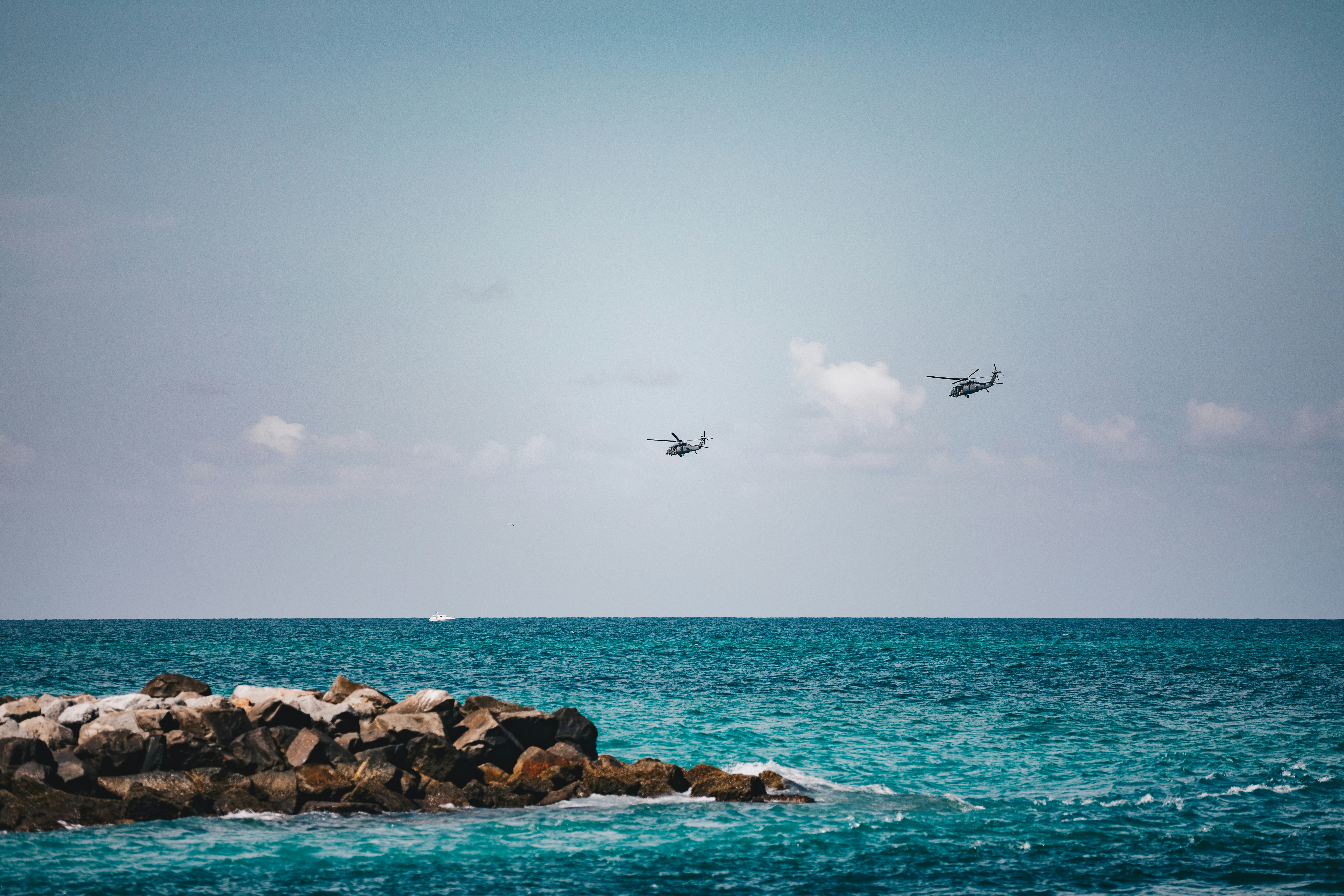Helicopters fly over the ocean near rocks. photo – Free Sea Image on ...