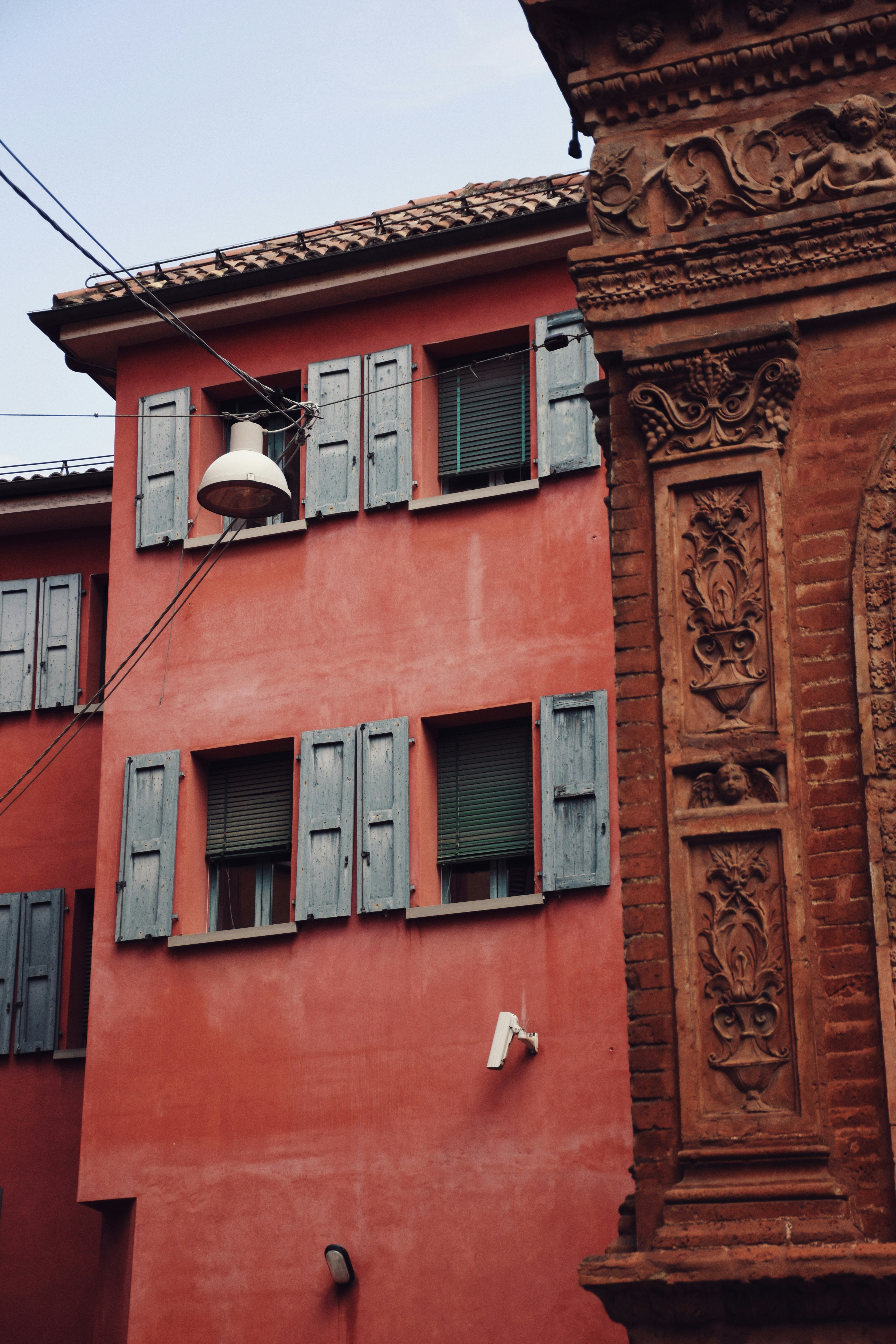A charming urban scene featuring a coral-colored building with teal shutters and intricate stonework, showcasing the blend of modern and historical architecture.