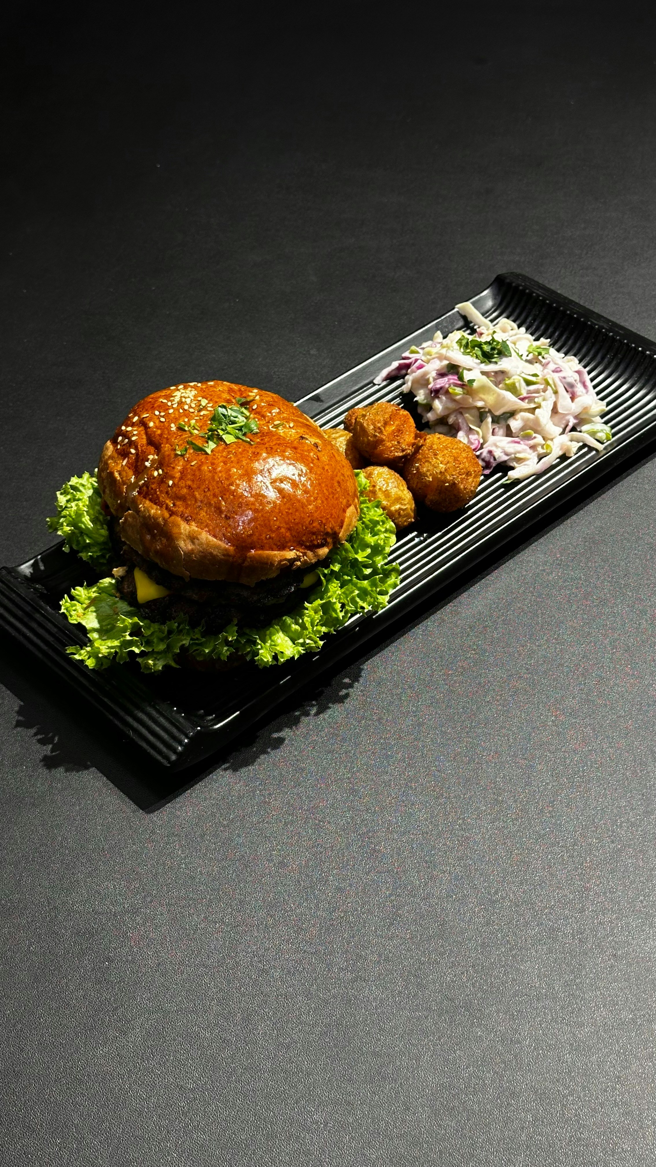 A gourmet burger garnished with fresh lettuce, accompanied by golden croquettes and a vibrant coleslaw. The artistic presentation highlights the dish's appeal.