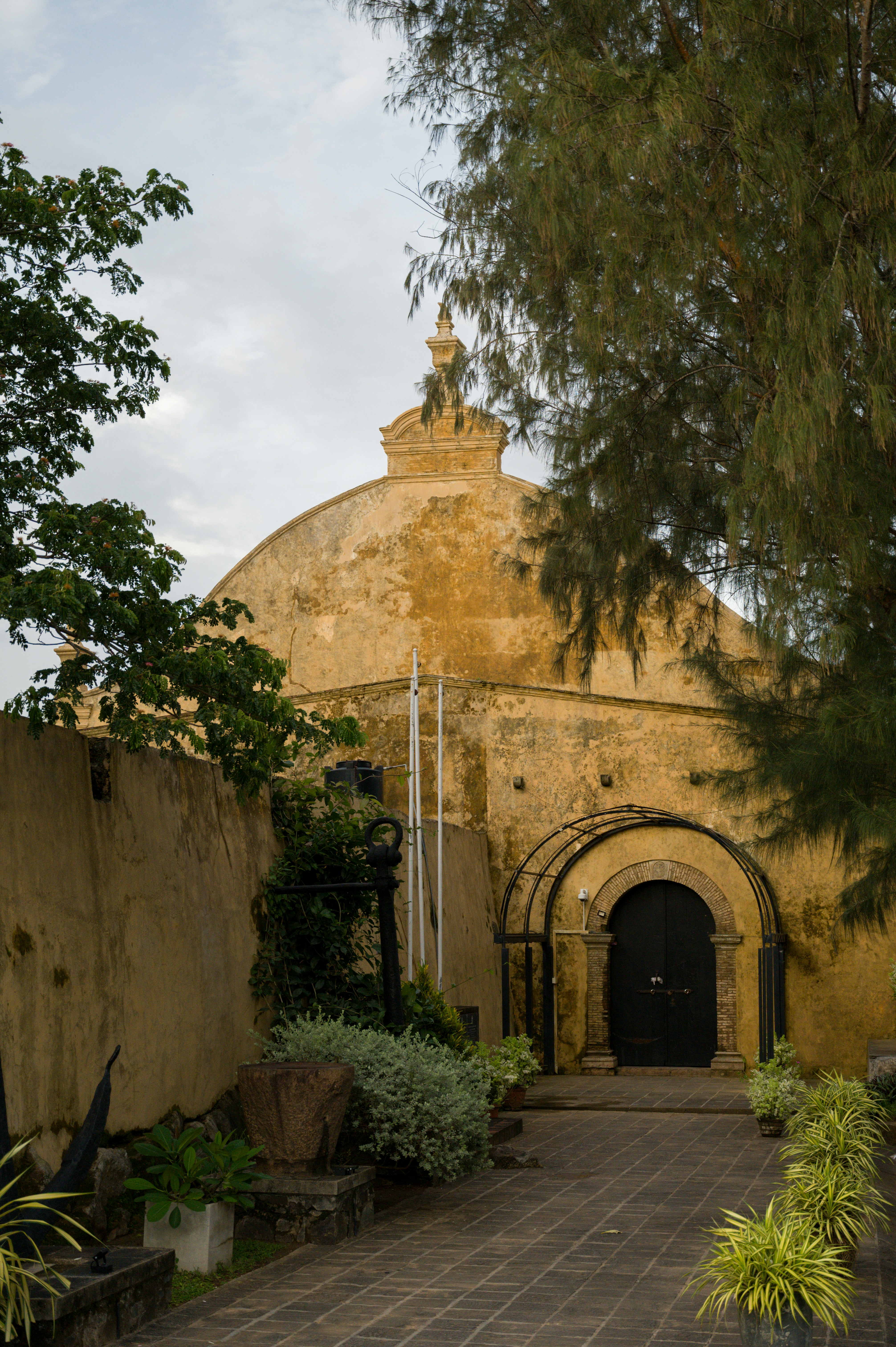 Weathered stone entrance to an ancient structure, framed by lush greenery and cobblestone path. A blend of nature and architectural heritage.