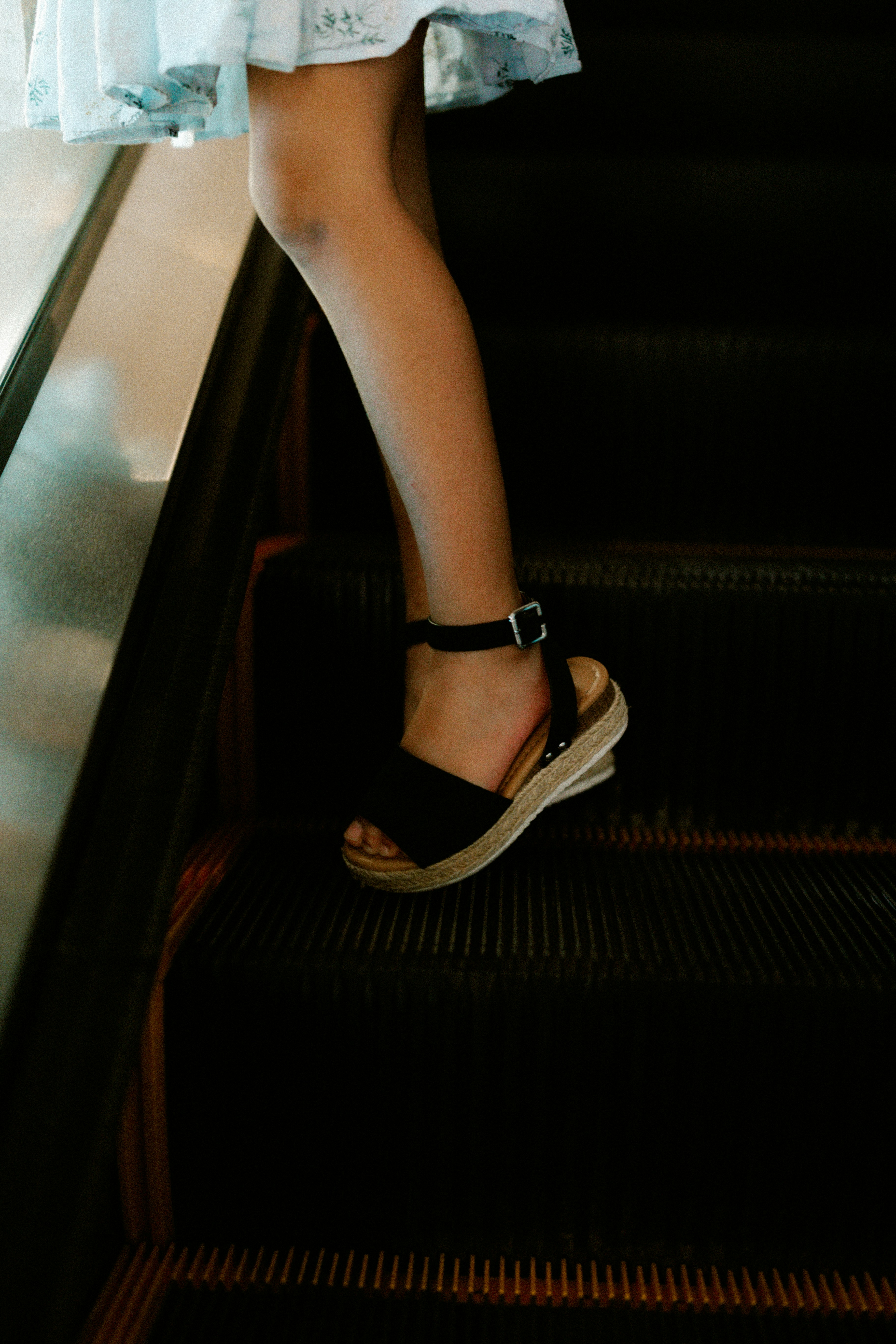 A child's foot steps onto an escalator.