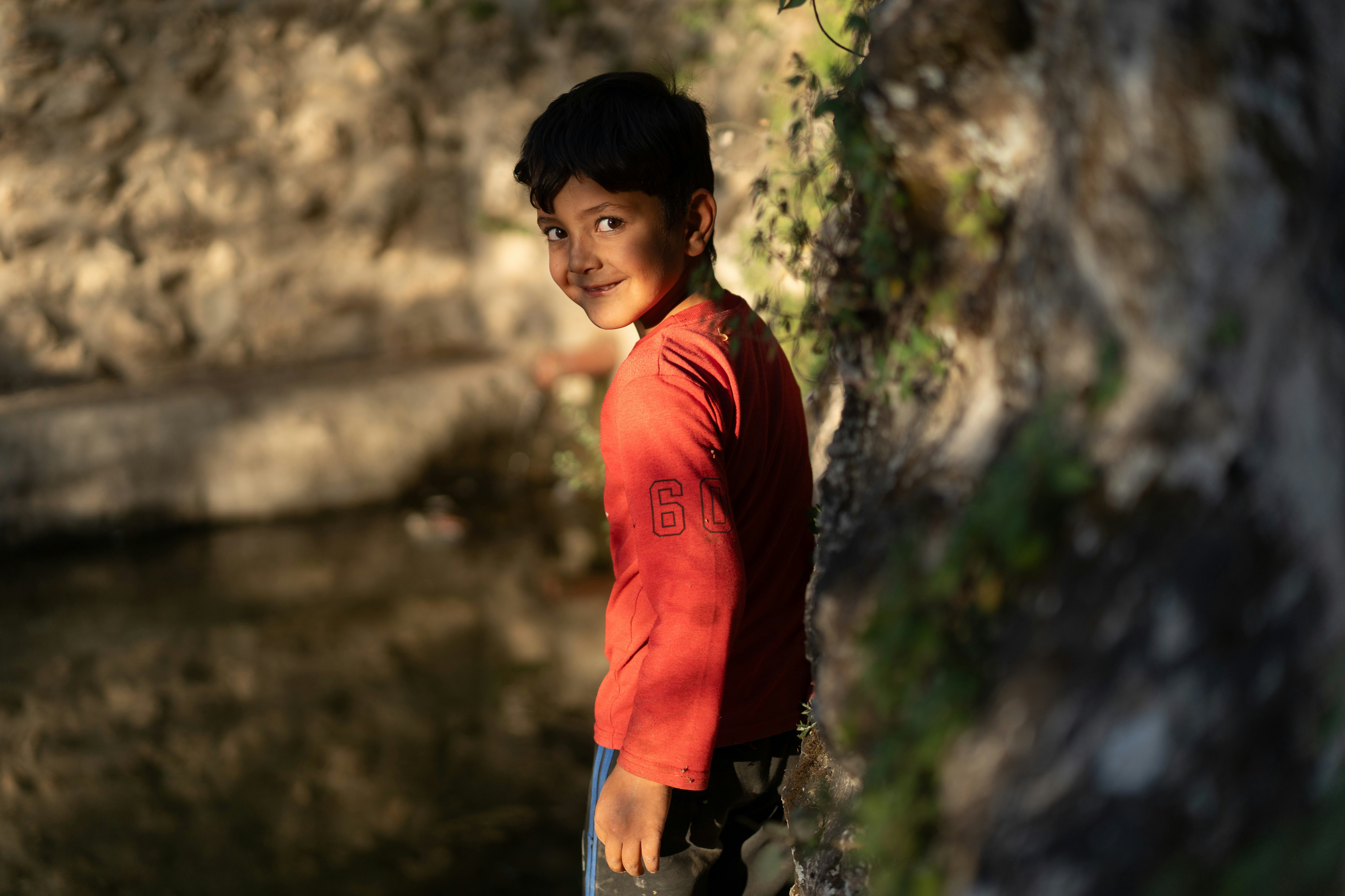 Child in Red by the Water: Quiet Gaze Amid Stone and Shadow