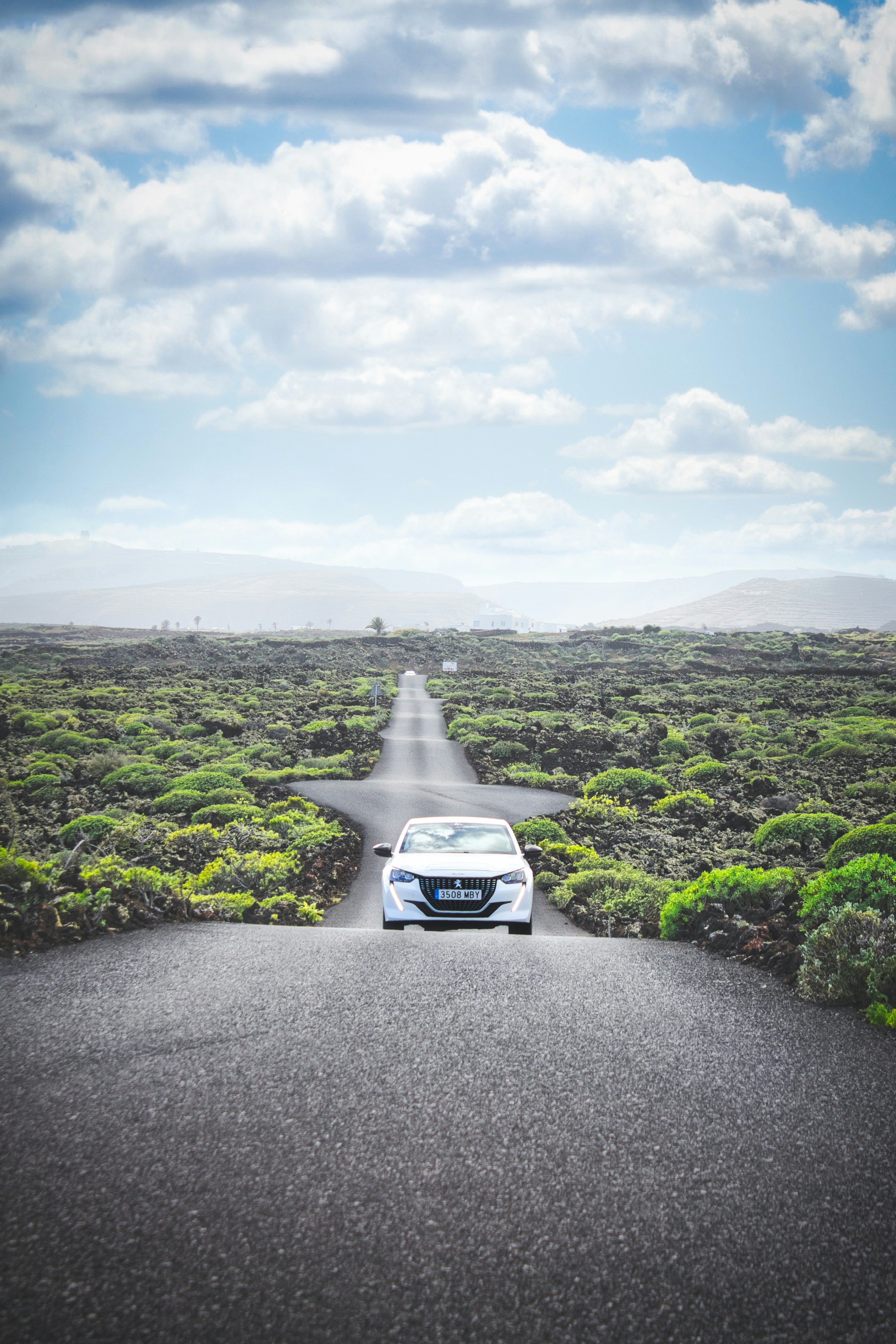Lava-Field Highway: A White Sedan Reaches the Cloudy Horizon