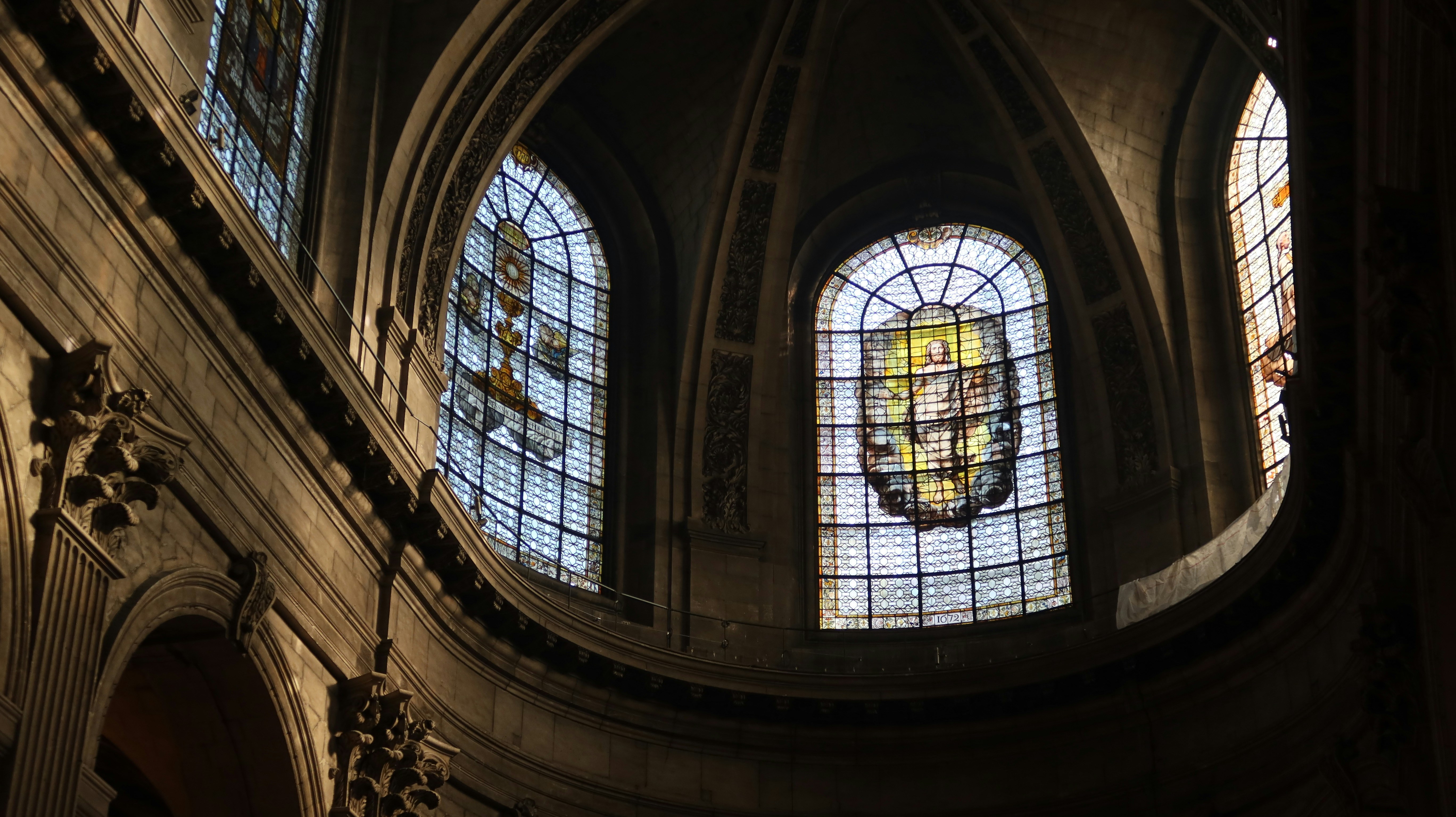 Intricate stained glass windows illuminate the curved architecture of a historic church interior, showcasing elaborate designs and warm light.