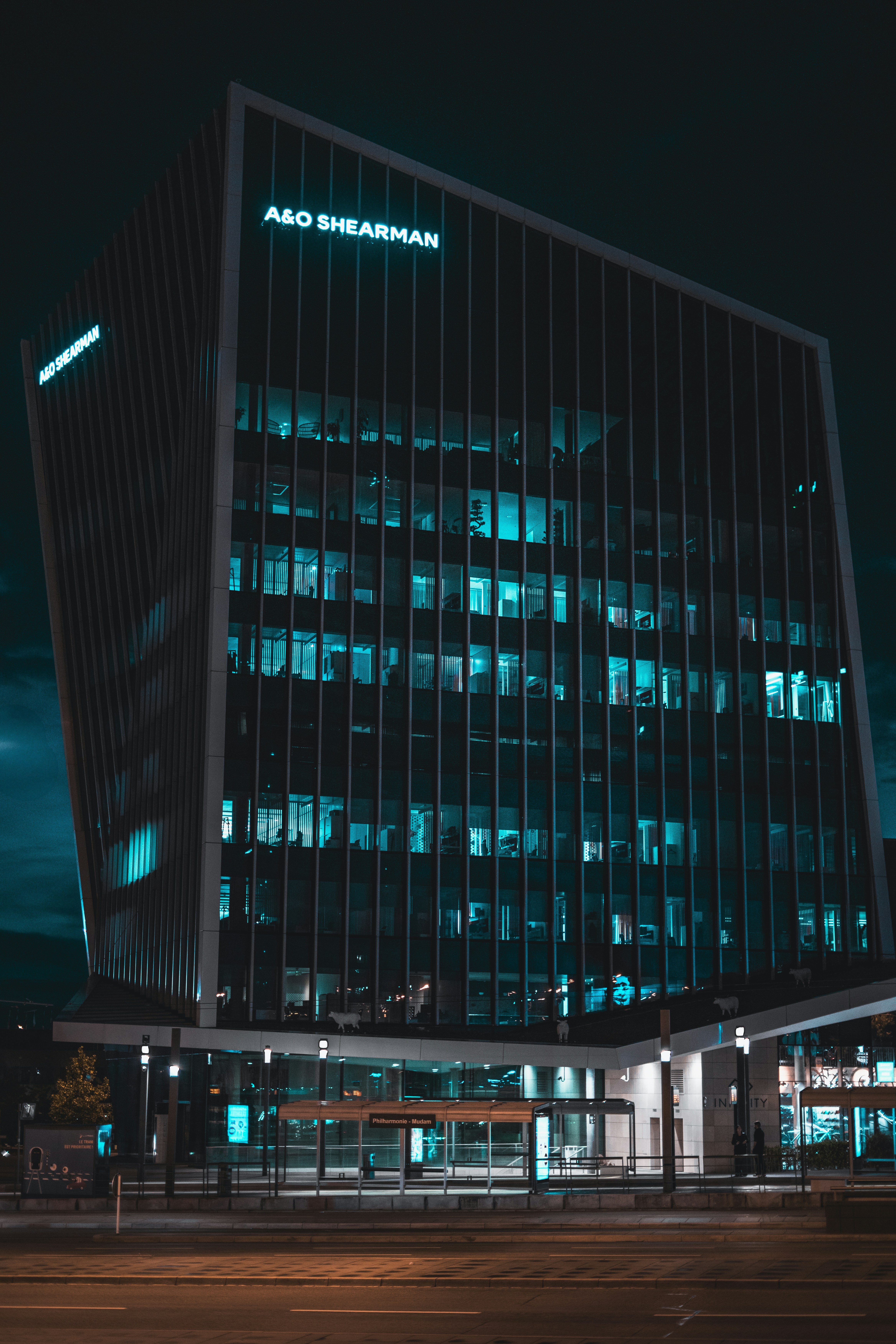 A sleek, modern office building illuminated in teal hues against a night sky, showcasing its glass facade and structural lines.