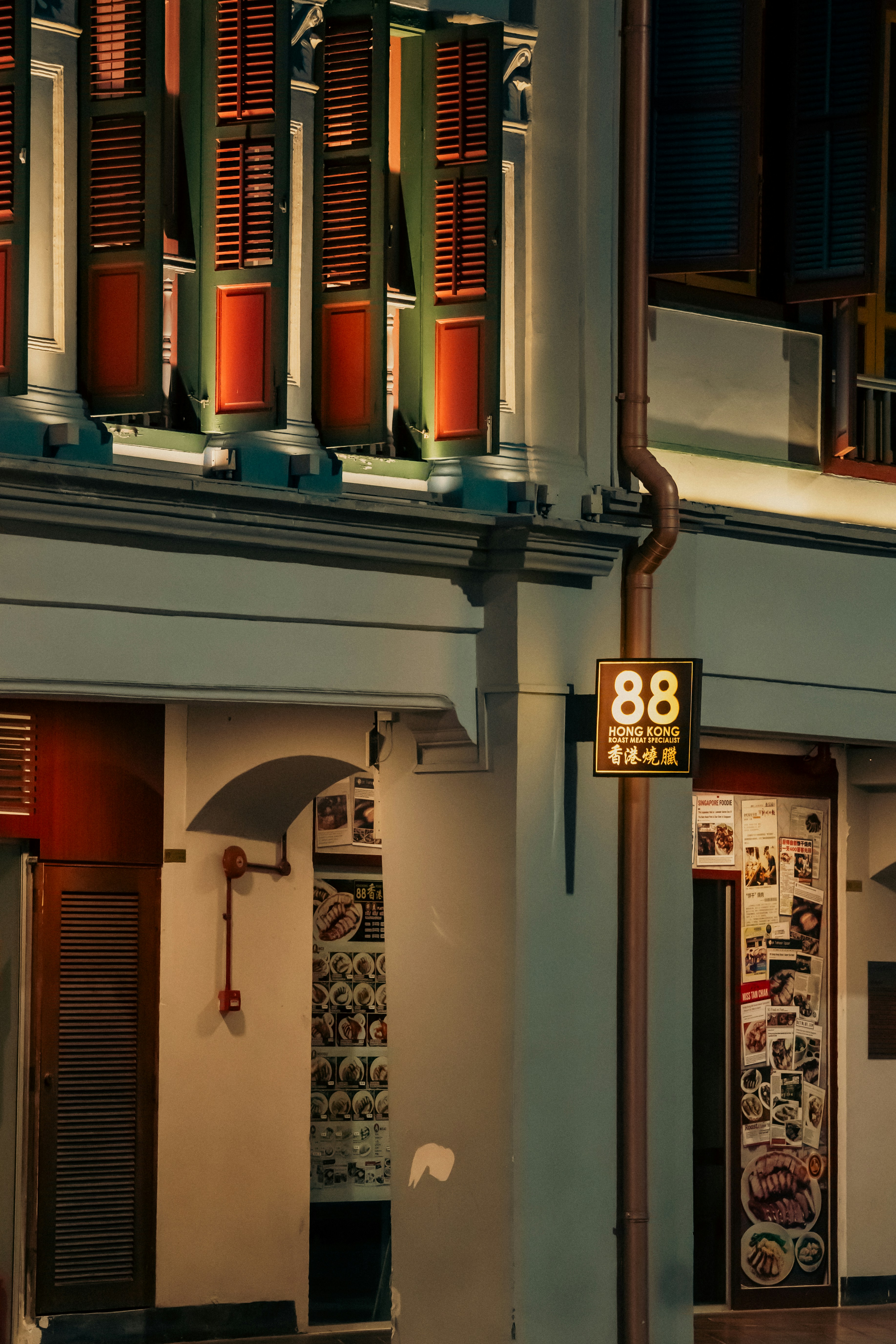 Colorful shophouse facade featuring intricate shutters and a prominent street sign in a bustling urban setting.