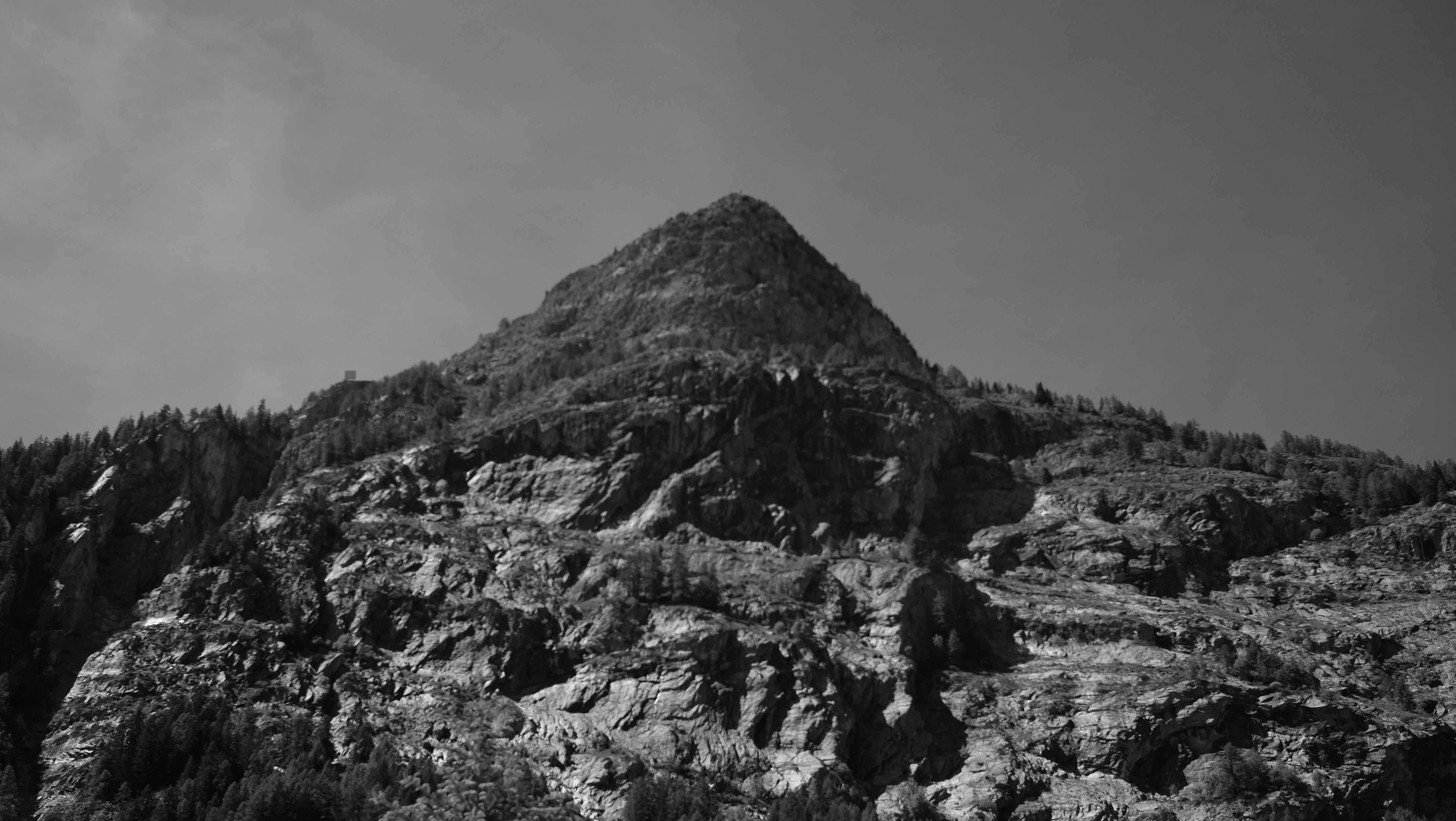 Dramatic black and white depiction of a towering mountain peak, showcasing rugged textures and stark contrasts against the sky.