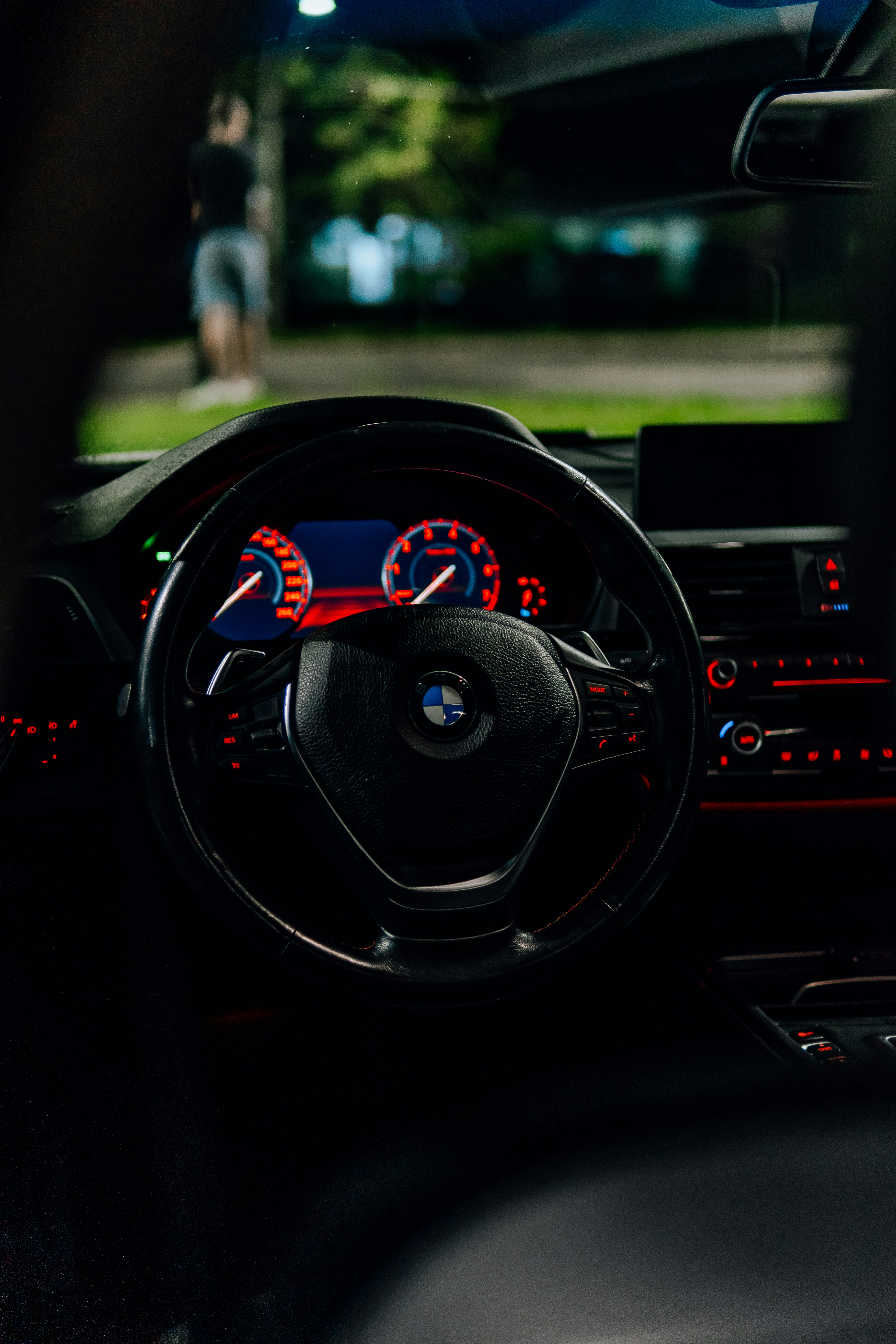 Interior view of a BMW car showcasing the illuminated dashboard and steering wheel, with a figure in the background. 