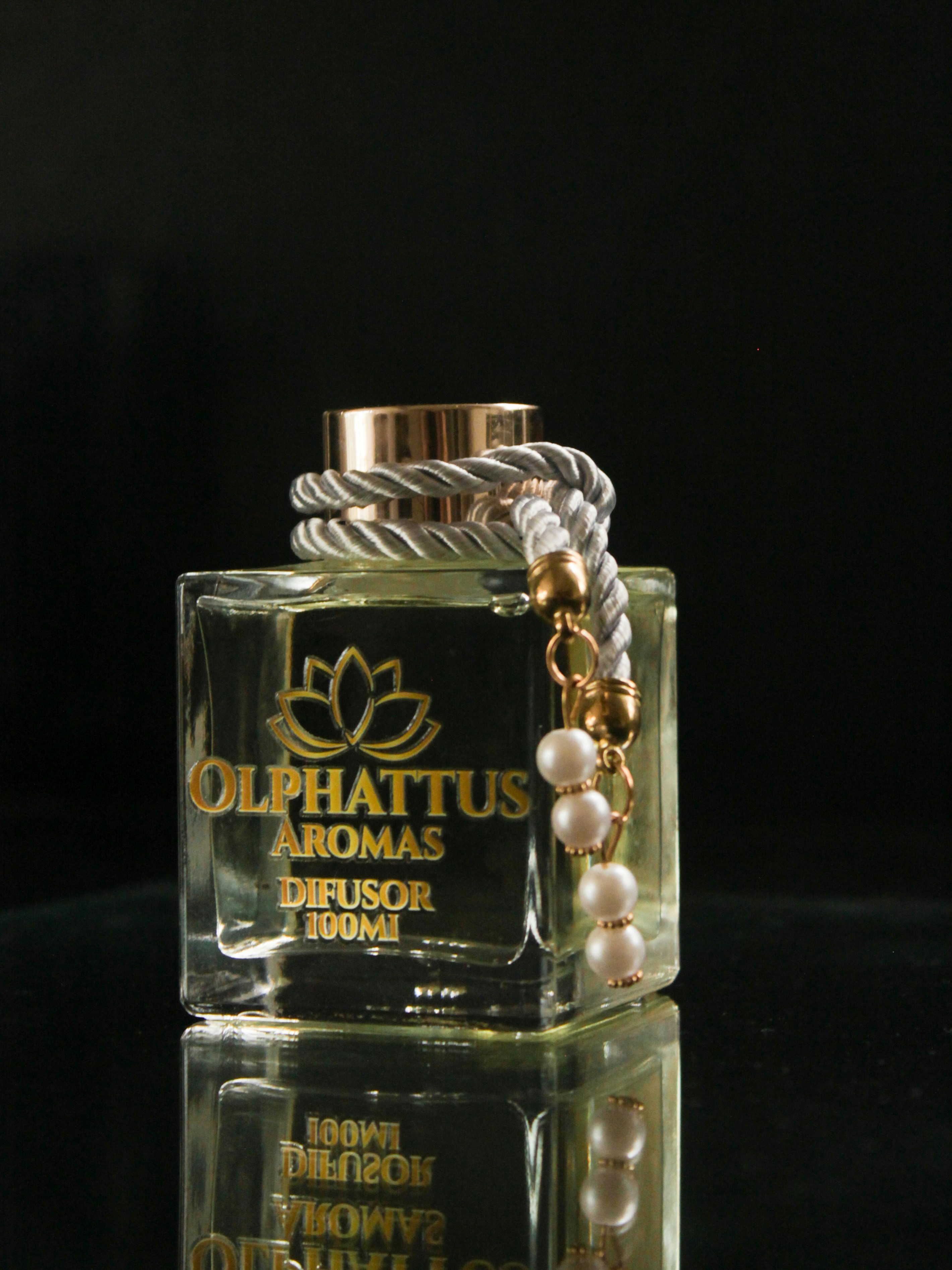 Elegant diffuser bottle adorned with a decorative rope and pearls, reflecting light against a dark background.