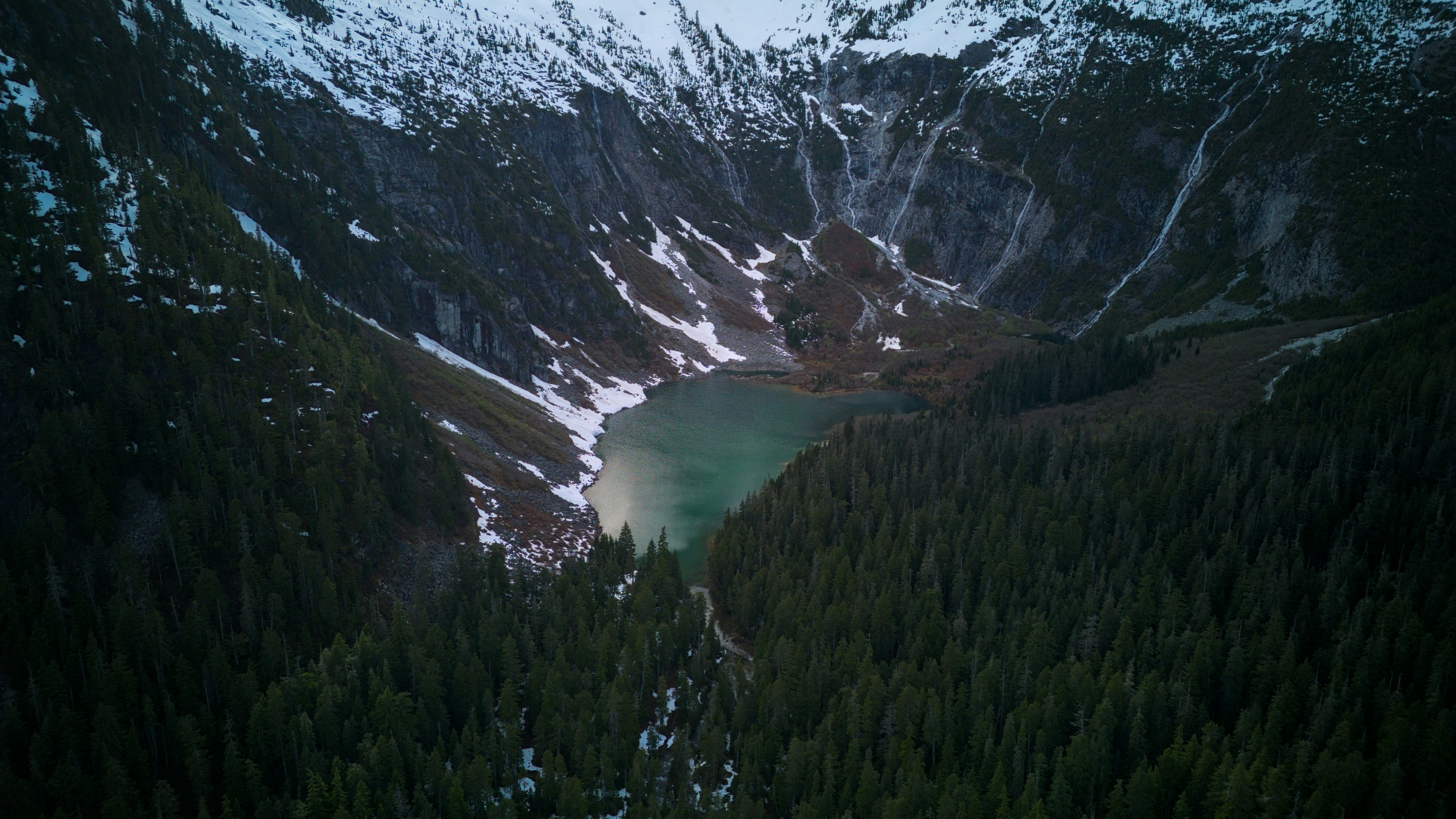 A tranquil alpine lake nestled within a rugged valley, surrounded by dense evergreen forests and snow-capped peaks. The scene captures the serene beauty of nature's untouched landscapes.