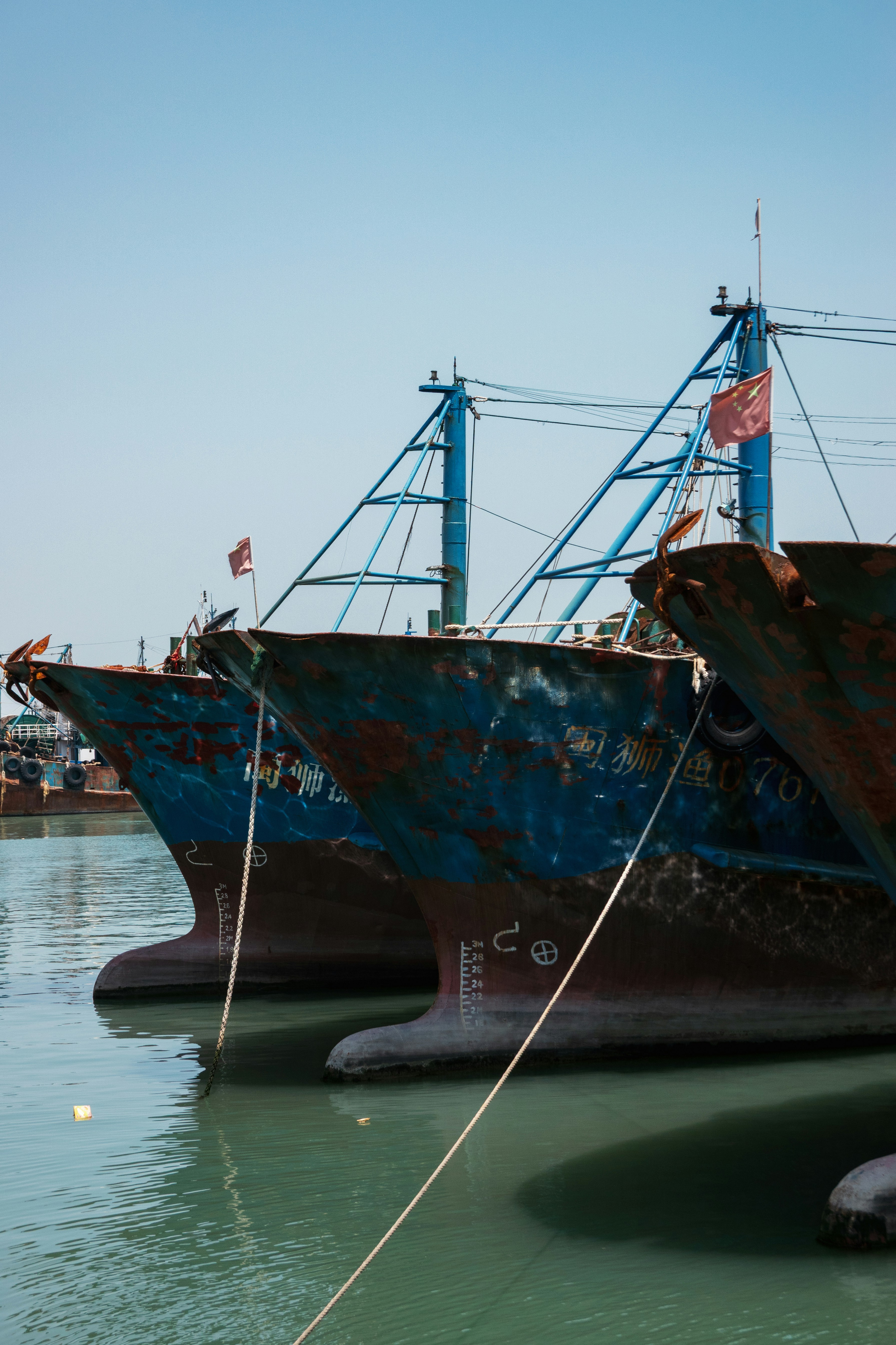 Three weathered fishing boats anchored in calm waters, showcasing rust and vibrant colors under a clear blue sky.