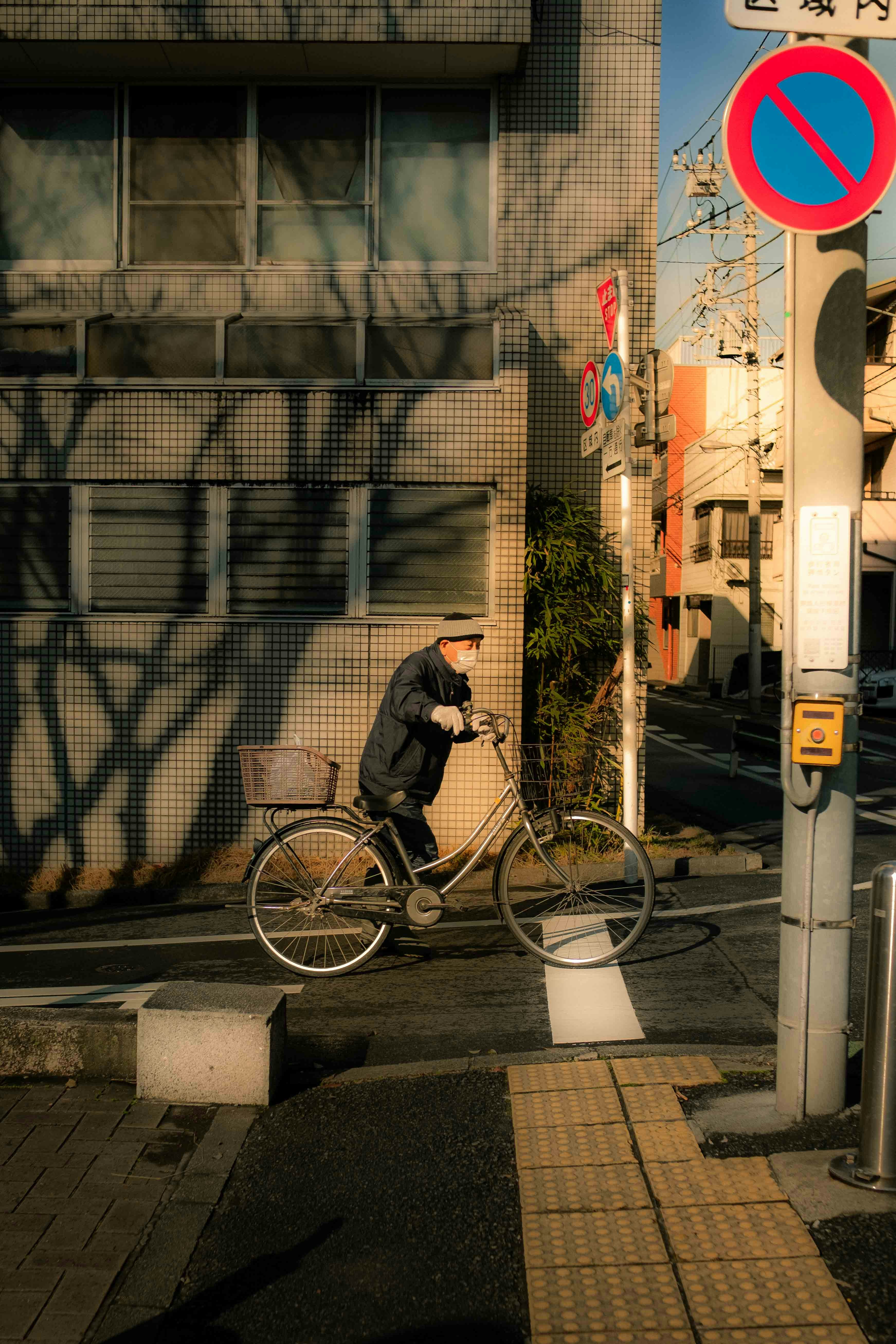 An elderly man riding a bicycle through a sunlit urban street, with shadows cast by nearby buildings creating a dynamic backdrop.