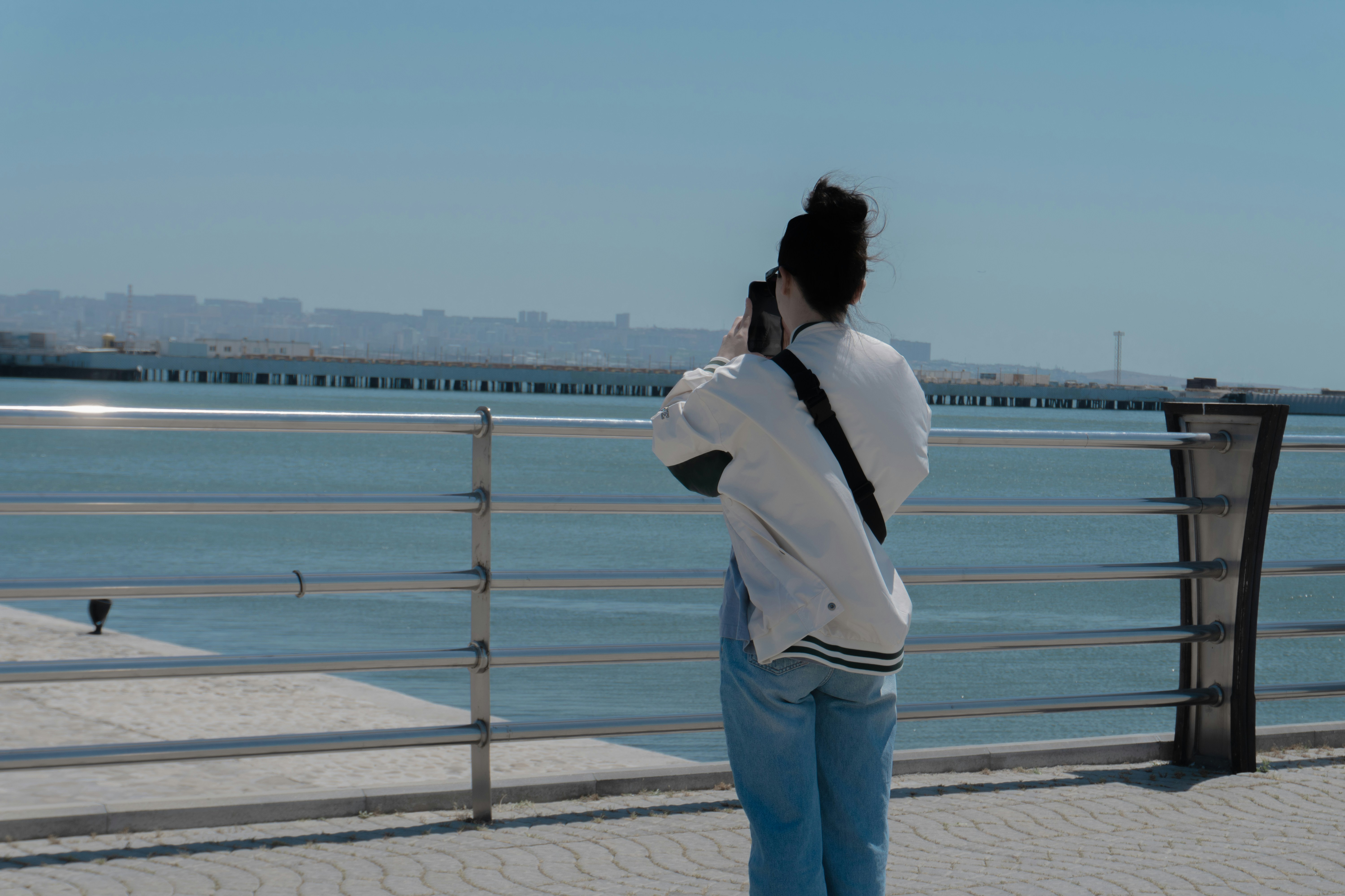 Beautiful young girl enjoys morning ambience at the Baku Boulevard | A woman takes a photo by the sea.