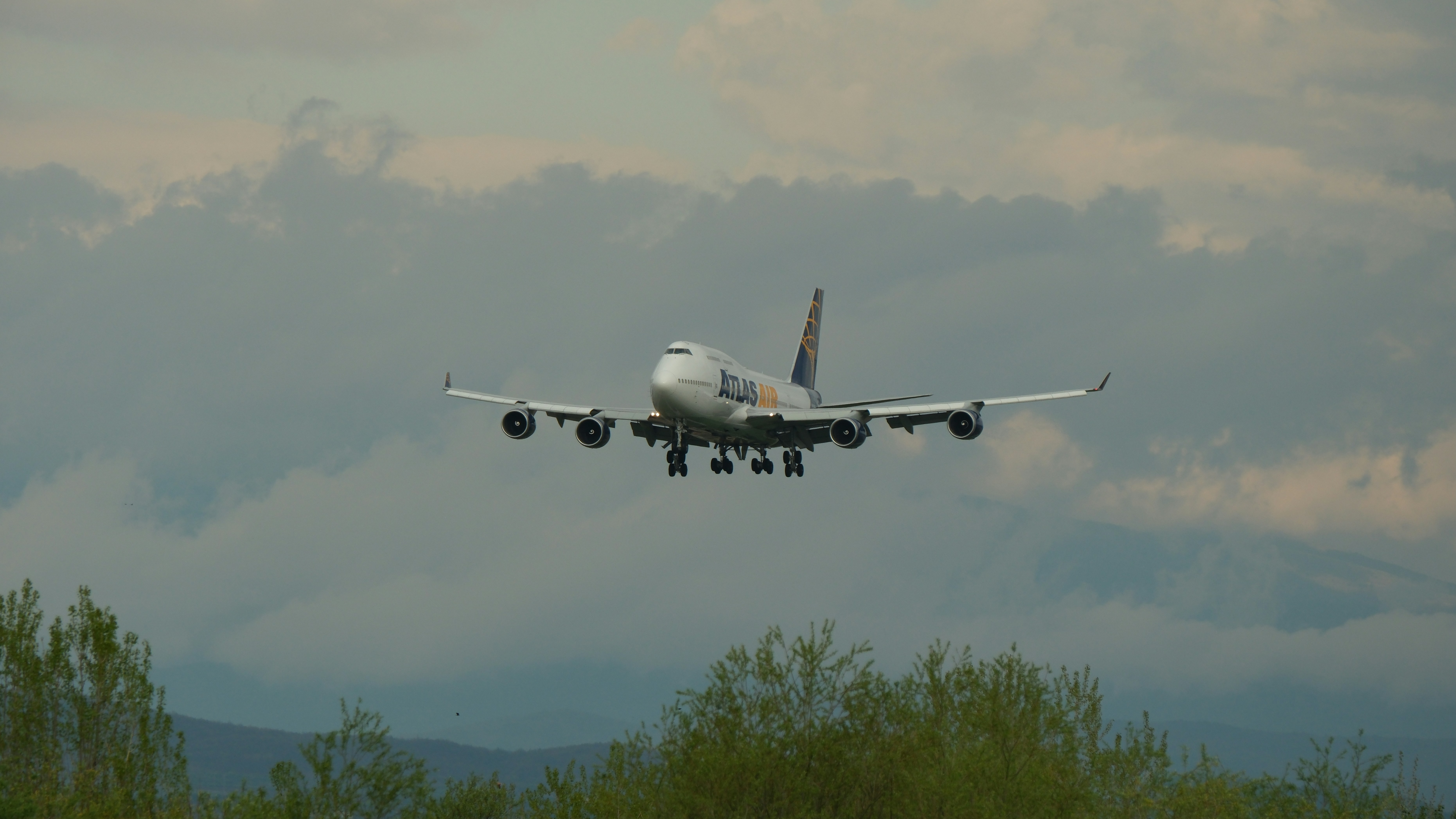 A large aircraft approaches landing amidst a backdrop of dramatic clouds and greenery, showcasing the intersection of technology and nature.