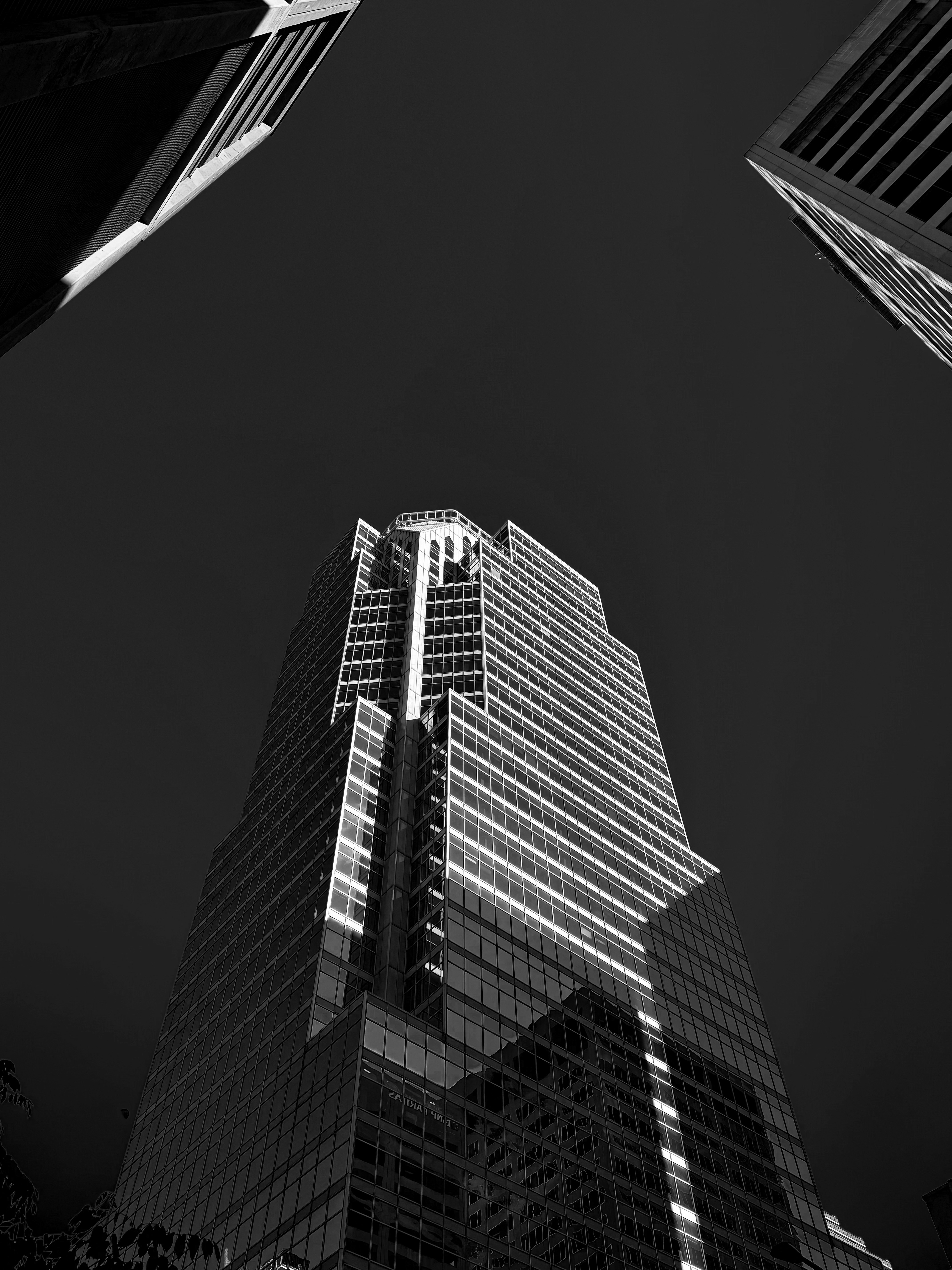 A towering skyscraper captured from below, showcasing its glass facade and geometric patterns against a dramatic black background.