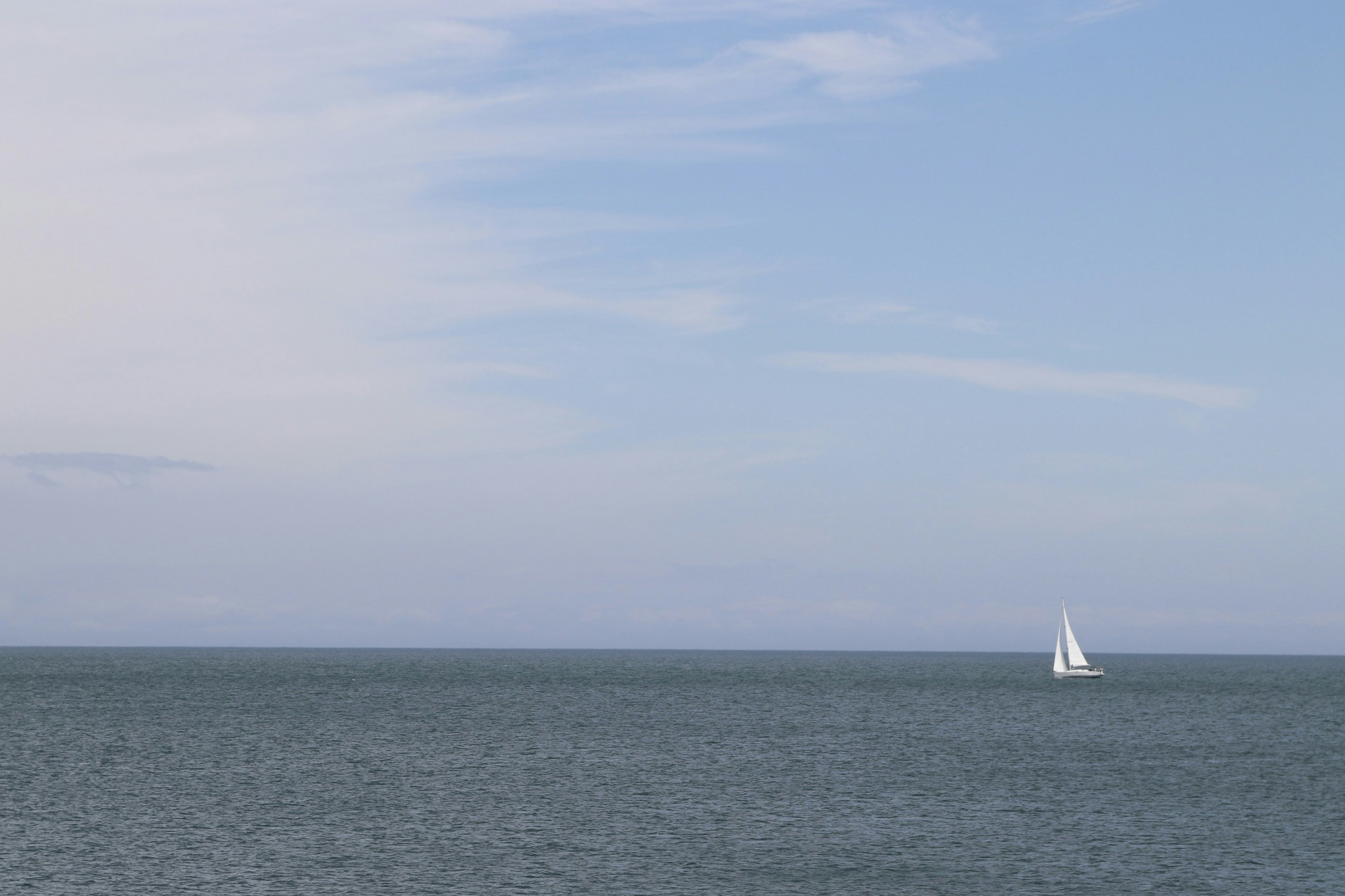 A solitary sailboat glides across a calm sea under a vast blue sky, embodying tranquility. The scene captures the essence of peaceful maritime exploration.