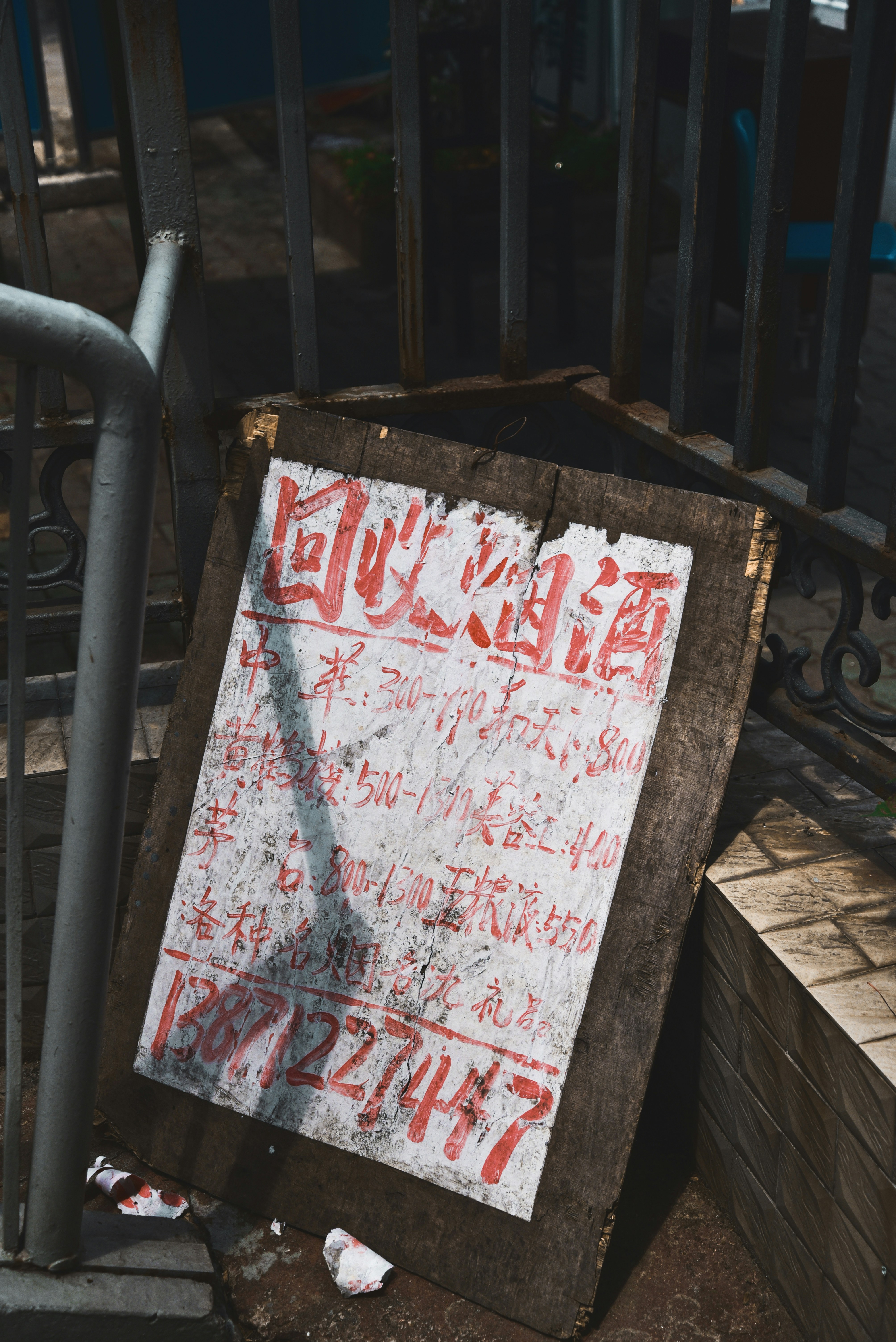 Weathered wooden sign displaying prices and contact information, partially obscured by urban elements.