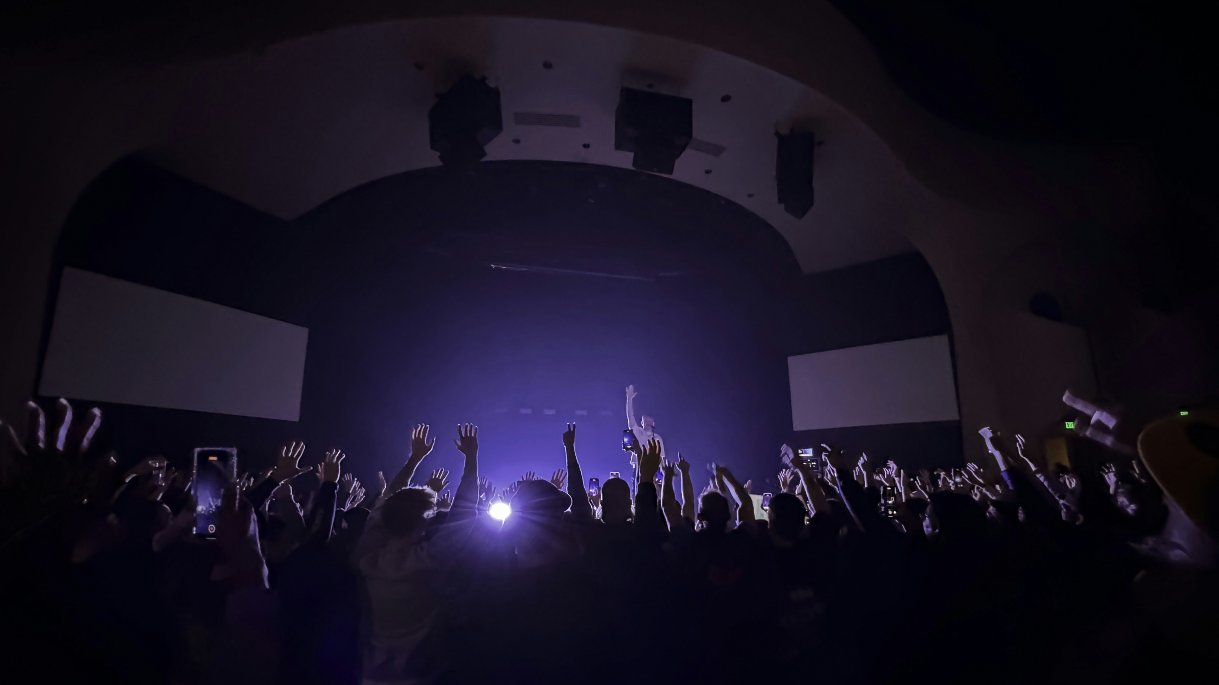 Crowd with raised hands immersed in a vibrant concert atmosphere, illuminated by dynamic stage lighting.