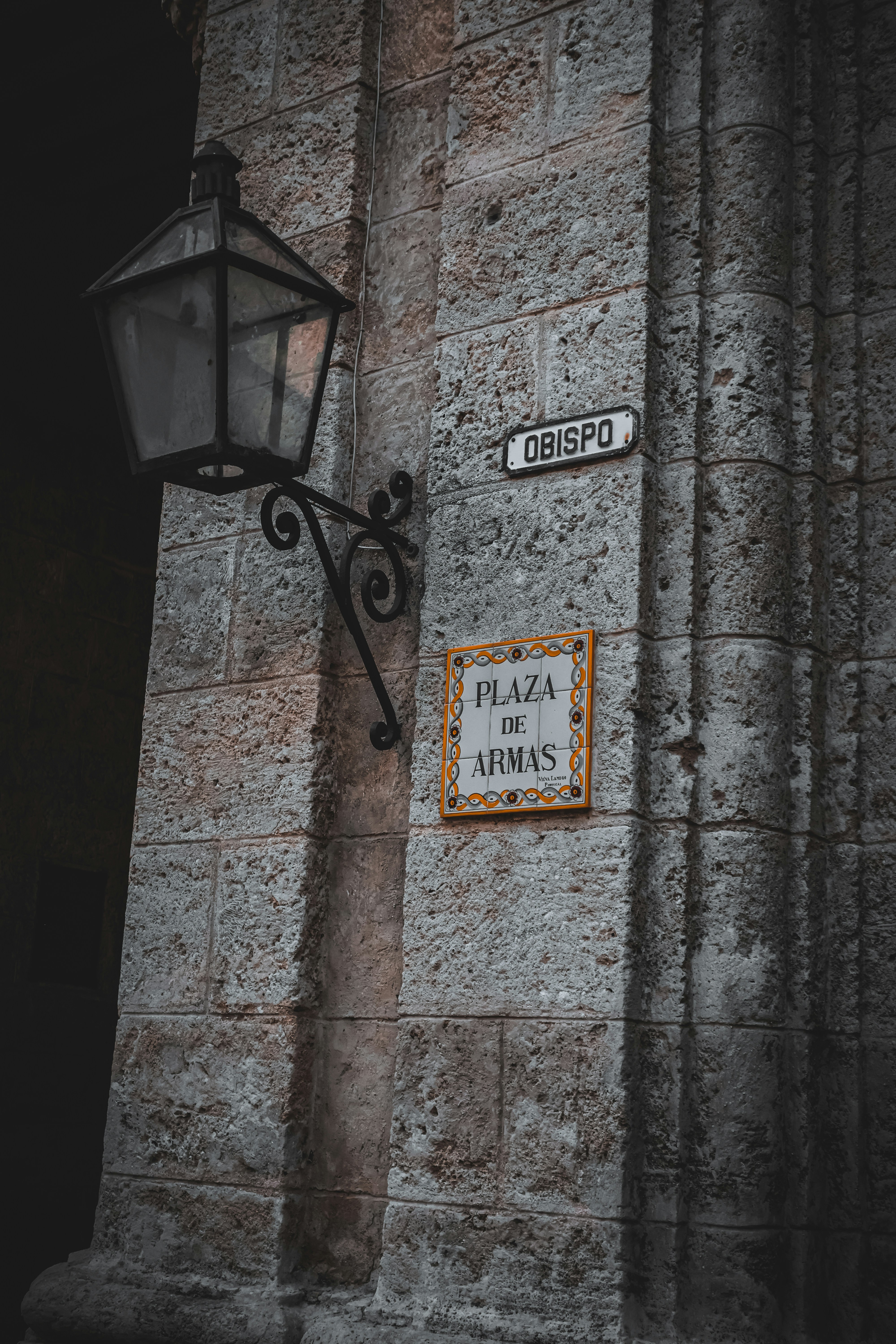 A stone wall features street signs and a lamp.